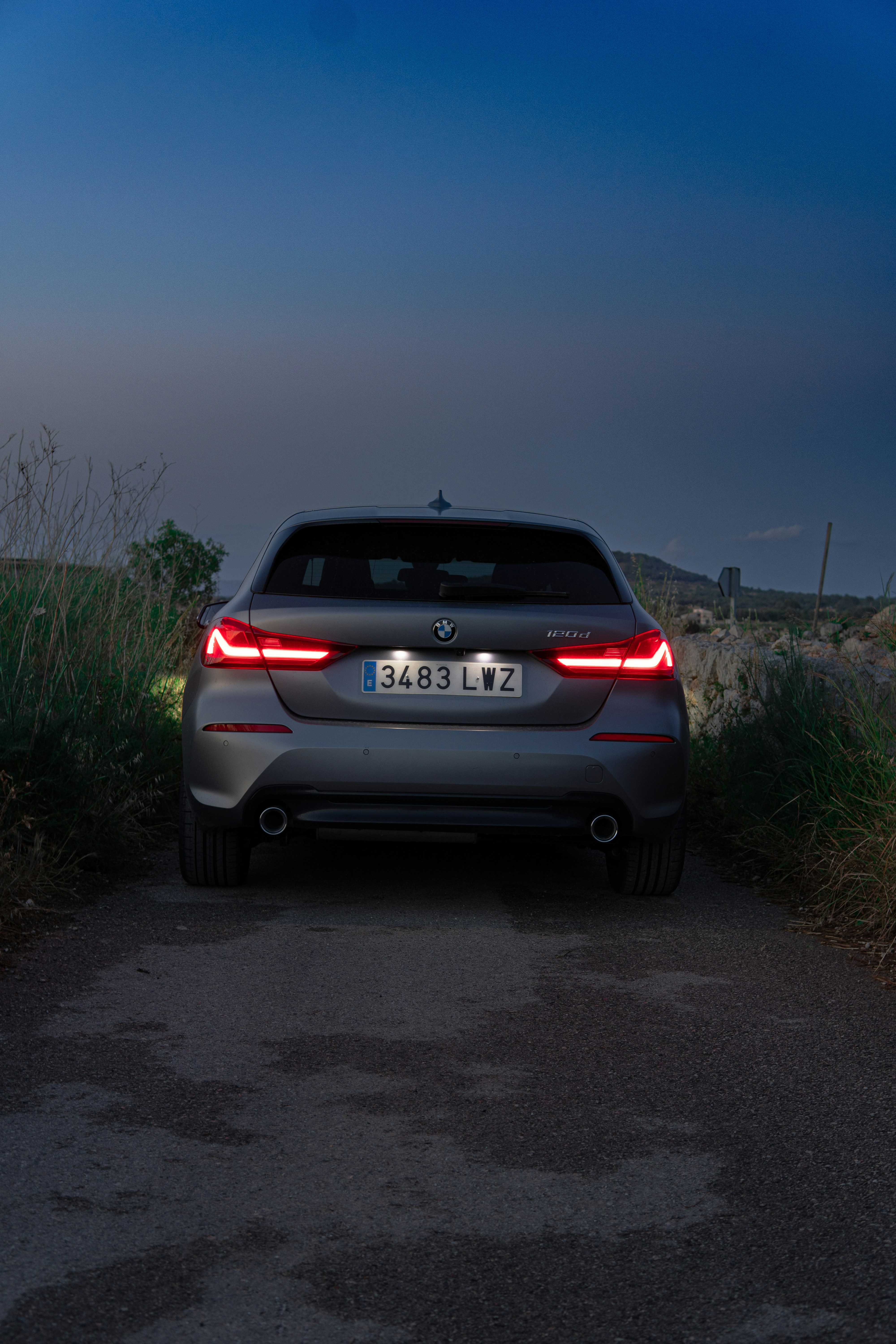 Dusk on a Narrow Backroad: BMW's Tail Lights Glow on a Quiet Gravel Lane