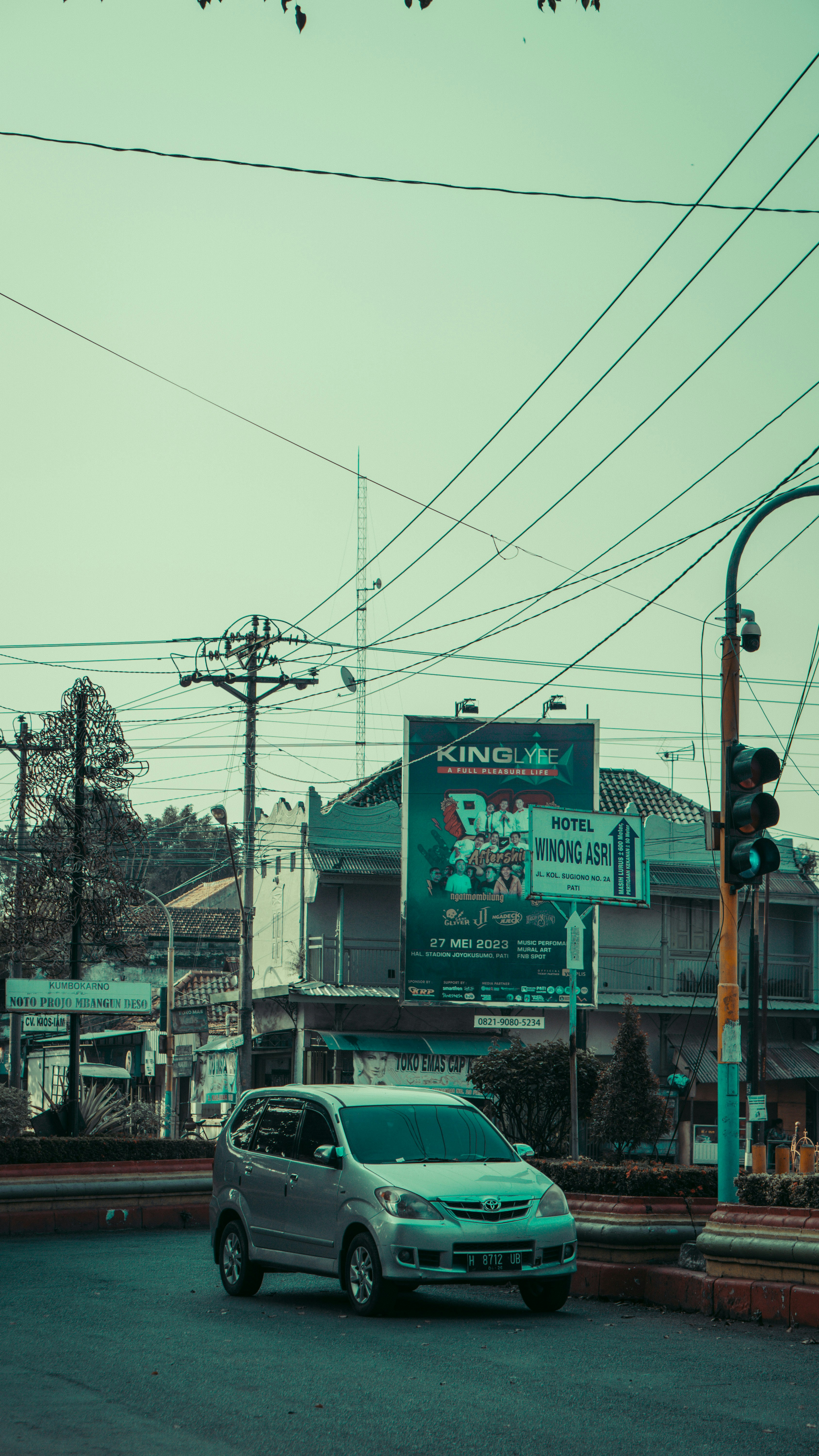 Silver Hatchback at the Tangle: Urban Street Under a Web of Wires