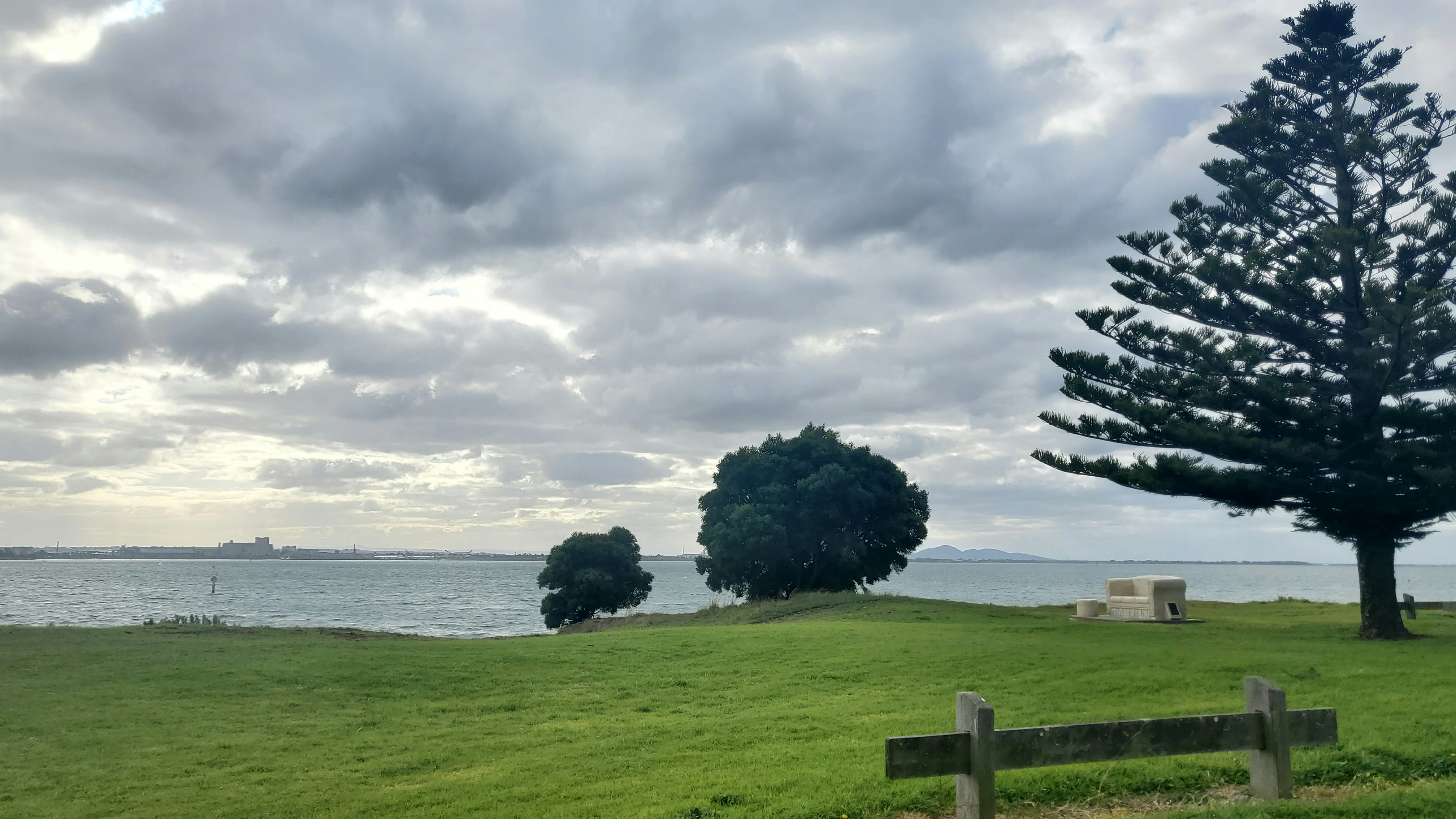 Cloud-laden sky over a grassy coastline with trees and distant ocean horizon.
