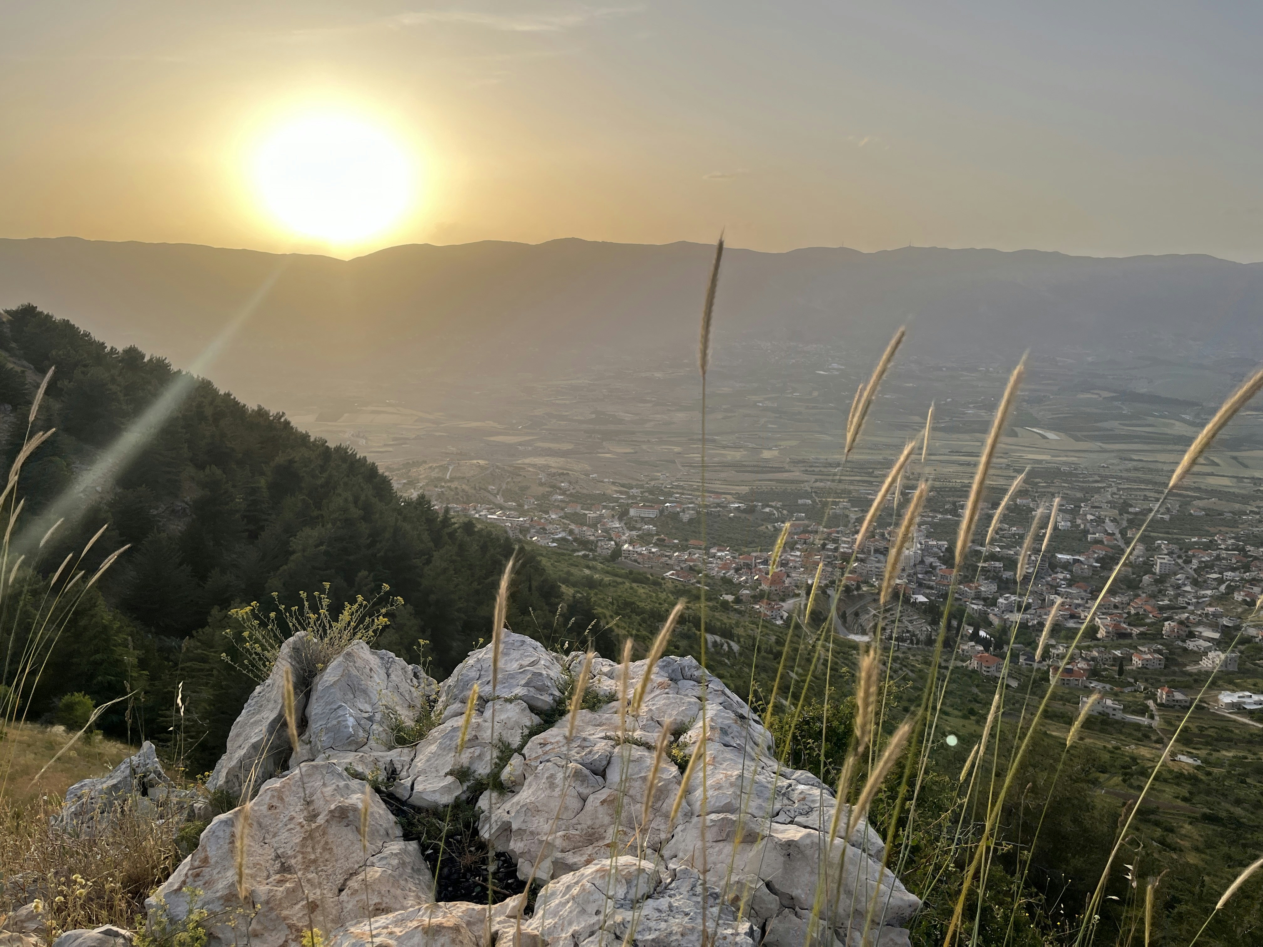 Golden sunset illuminating a valley with rocky foreground and distant town.