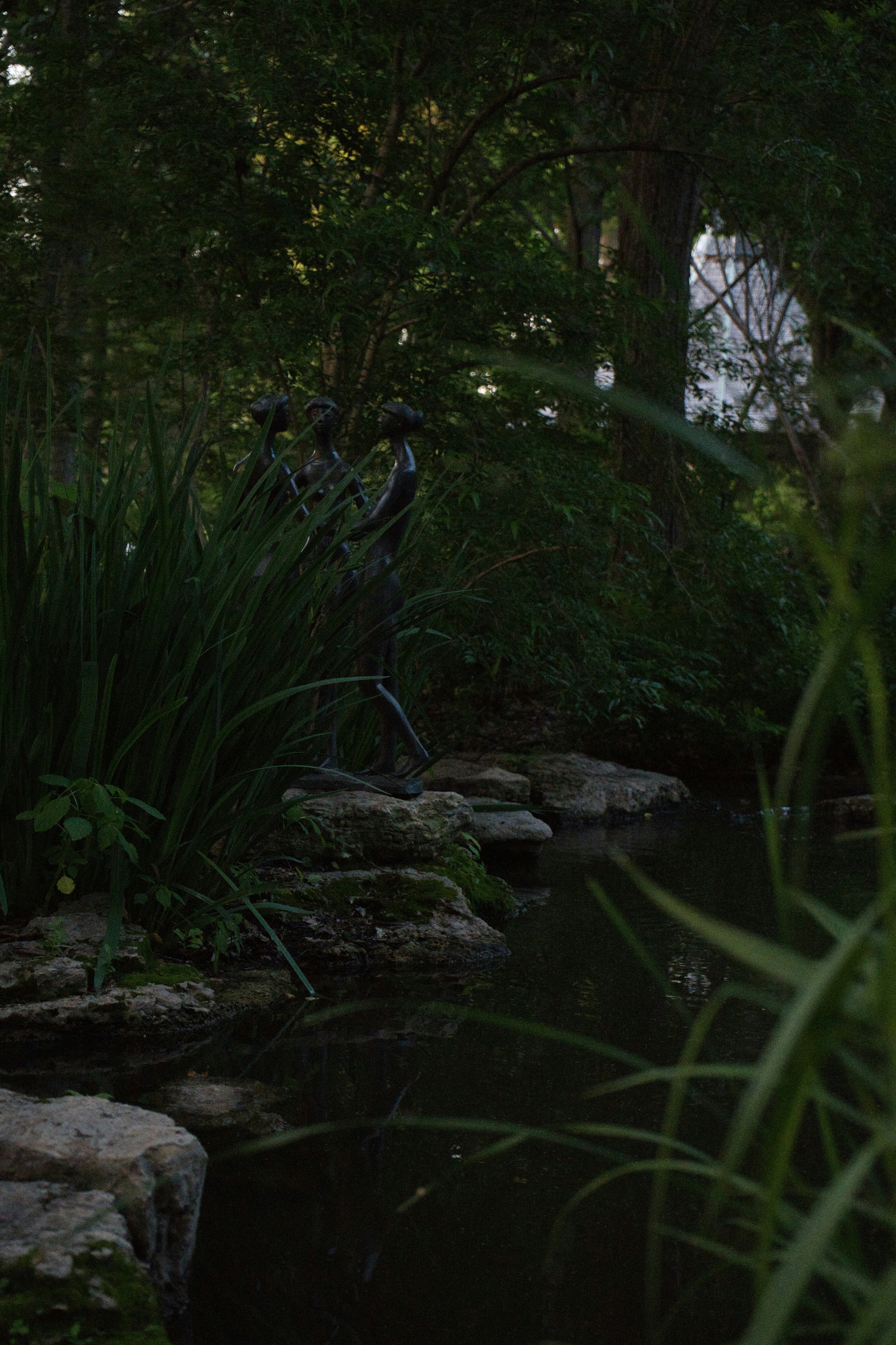 Three Shadowed Figures Guard a Quiet Garden Stream