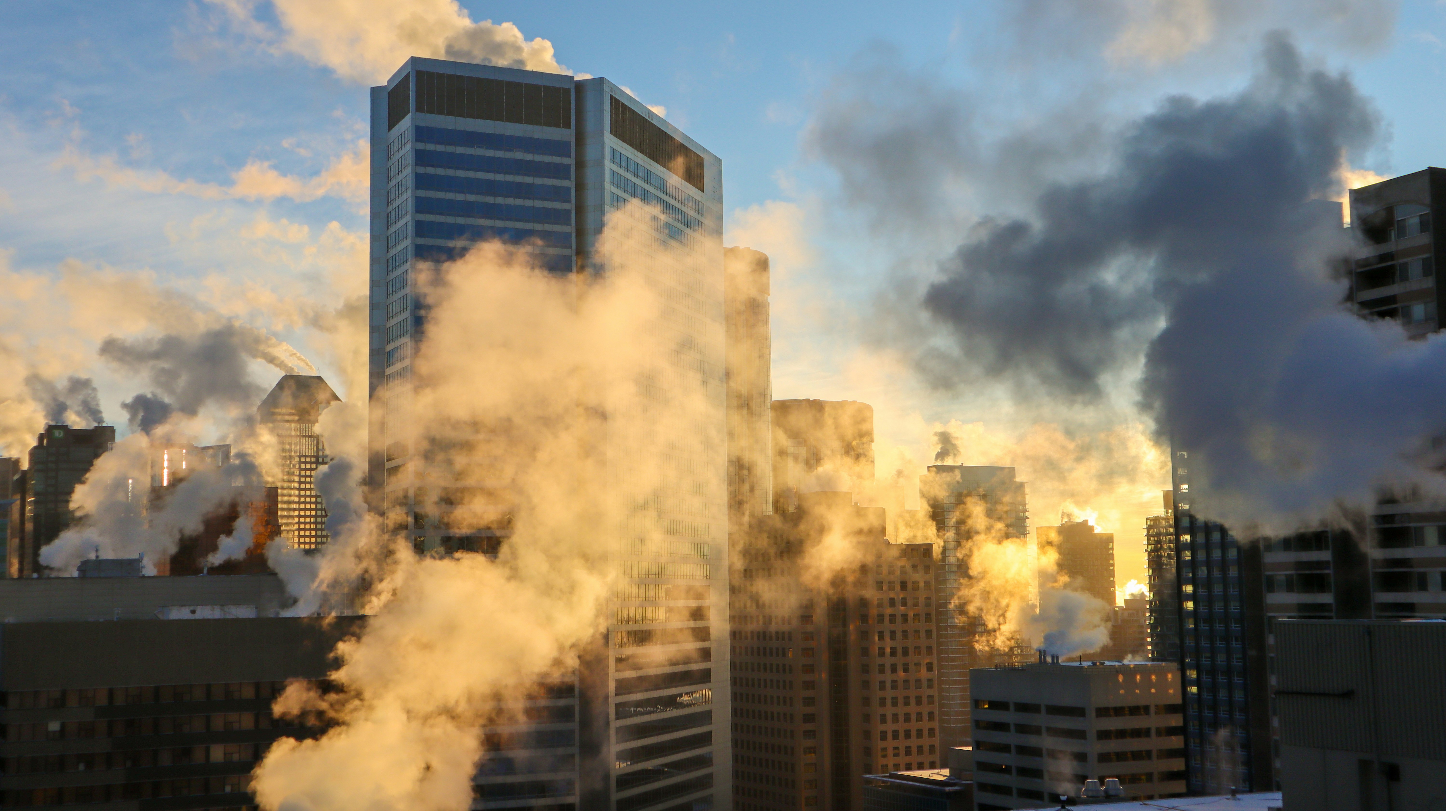 Steam rises from buildings against a sunrise backdrop in a cityscape.