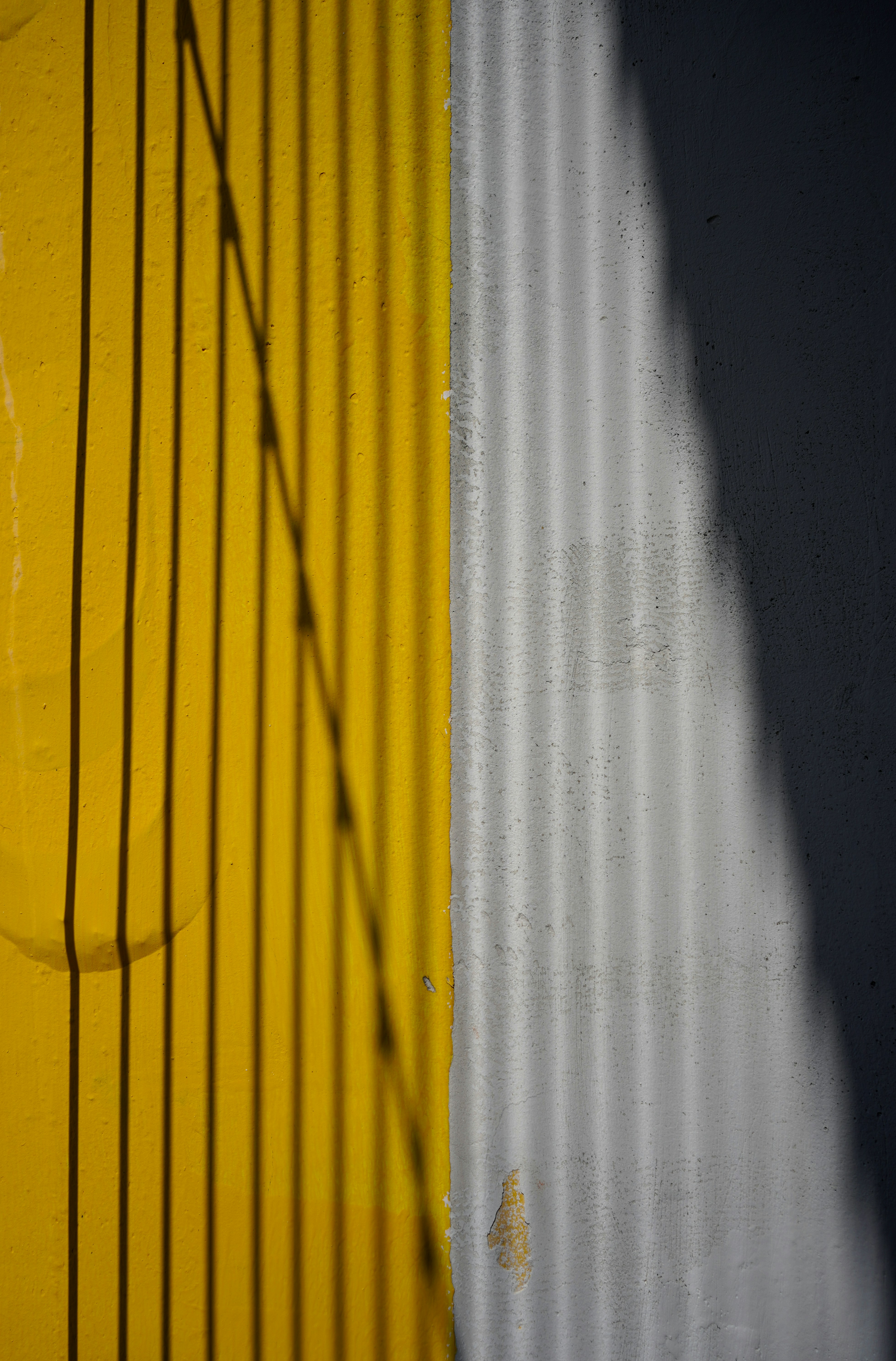 Split by Shadow: Yellow Barrier Meets a Grey Corrugated Wall