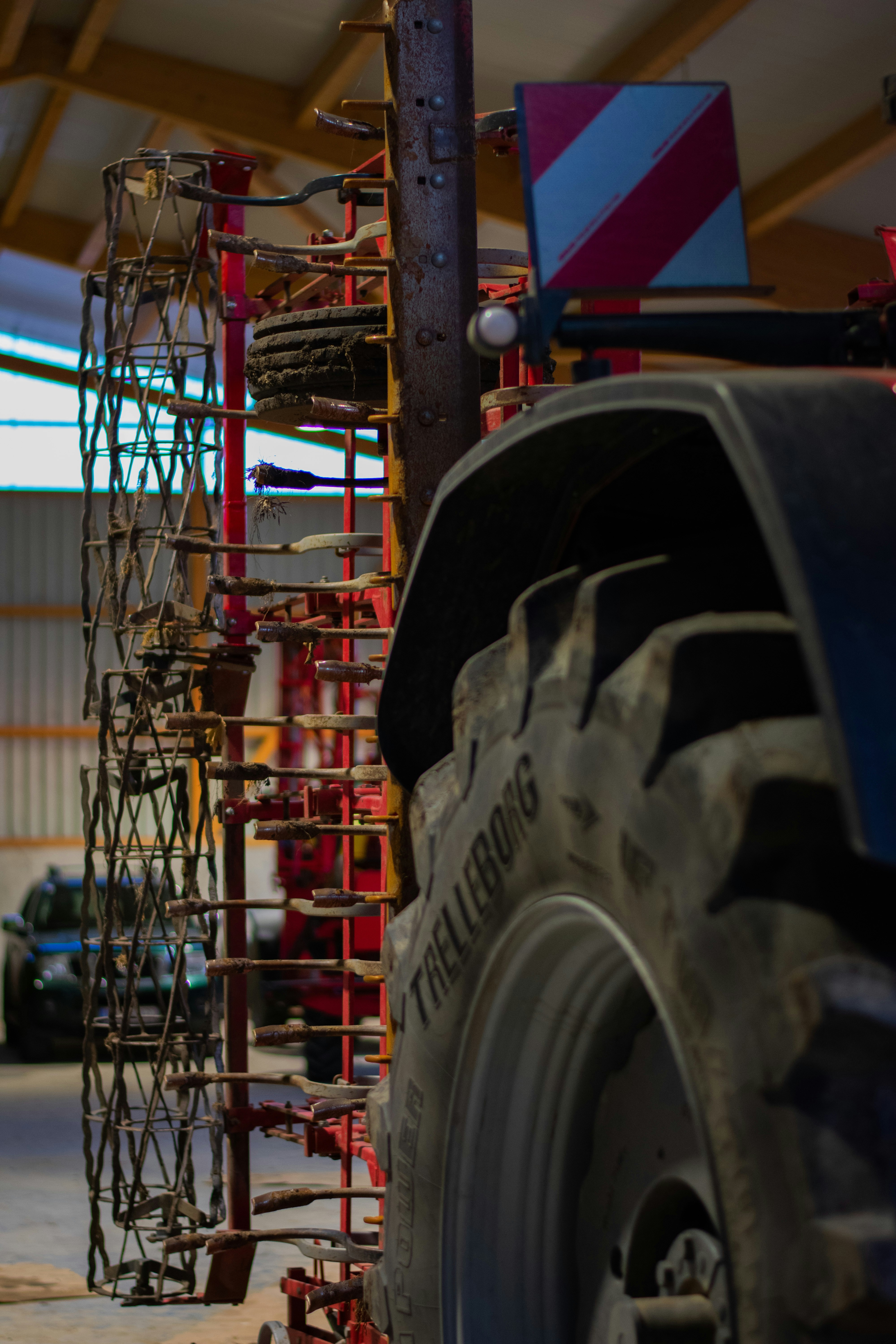 Close-up of a tractor's tire and attached equipment in a barn setting, showcasing agricultural tools and machinery. 