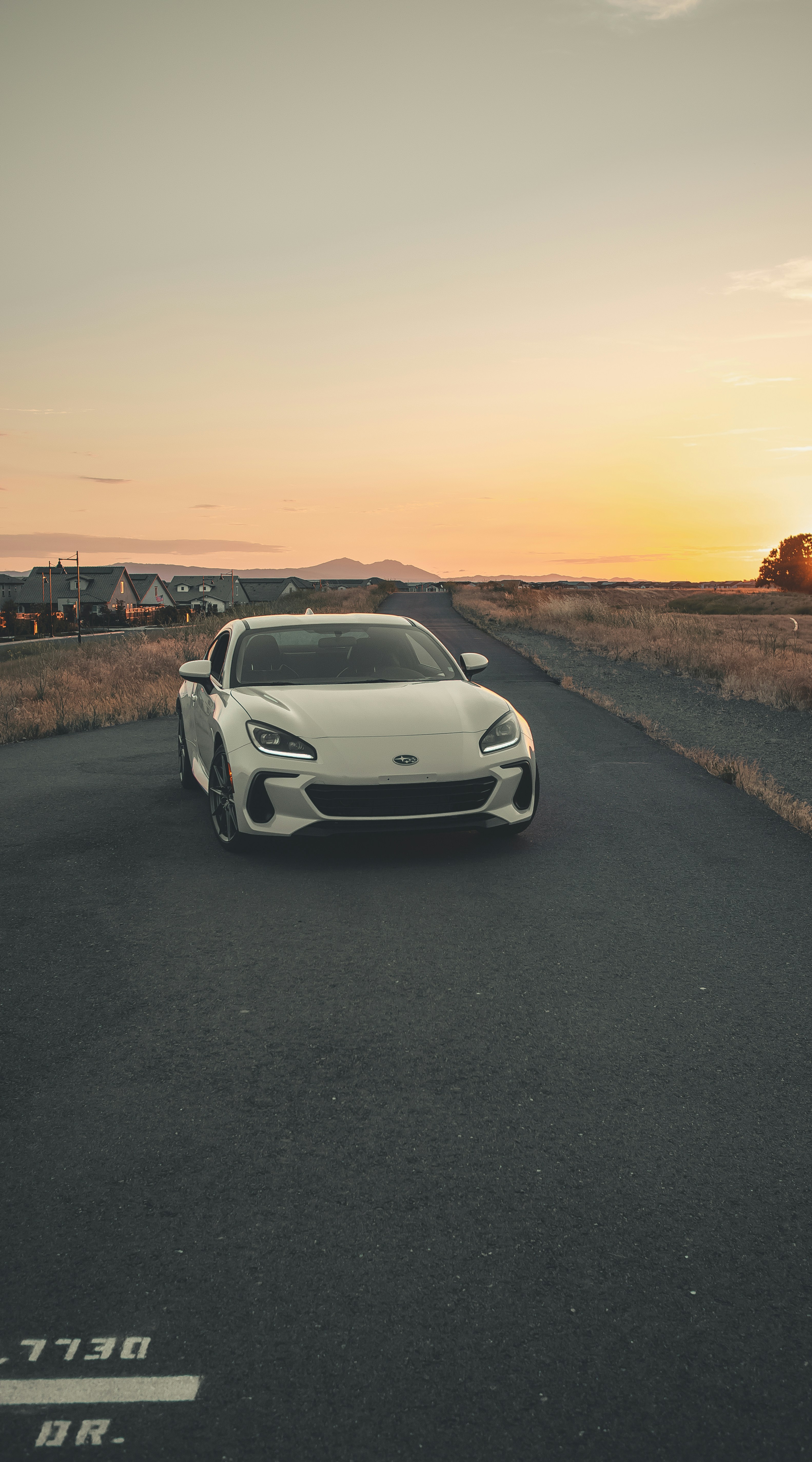 White sports coupe on a rural road at sunset