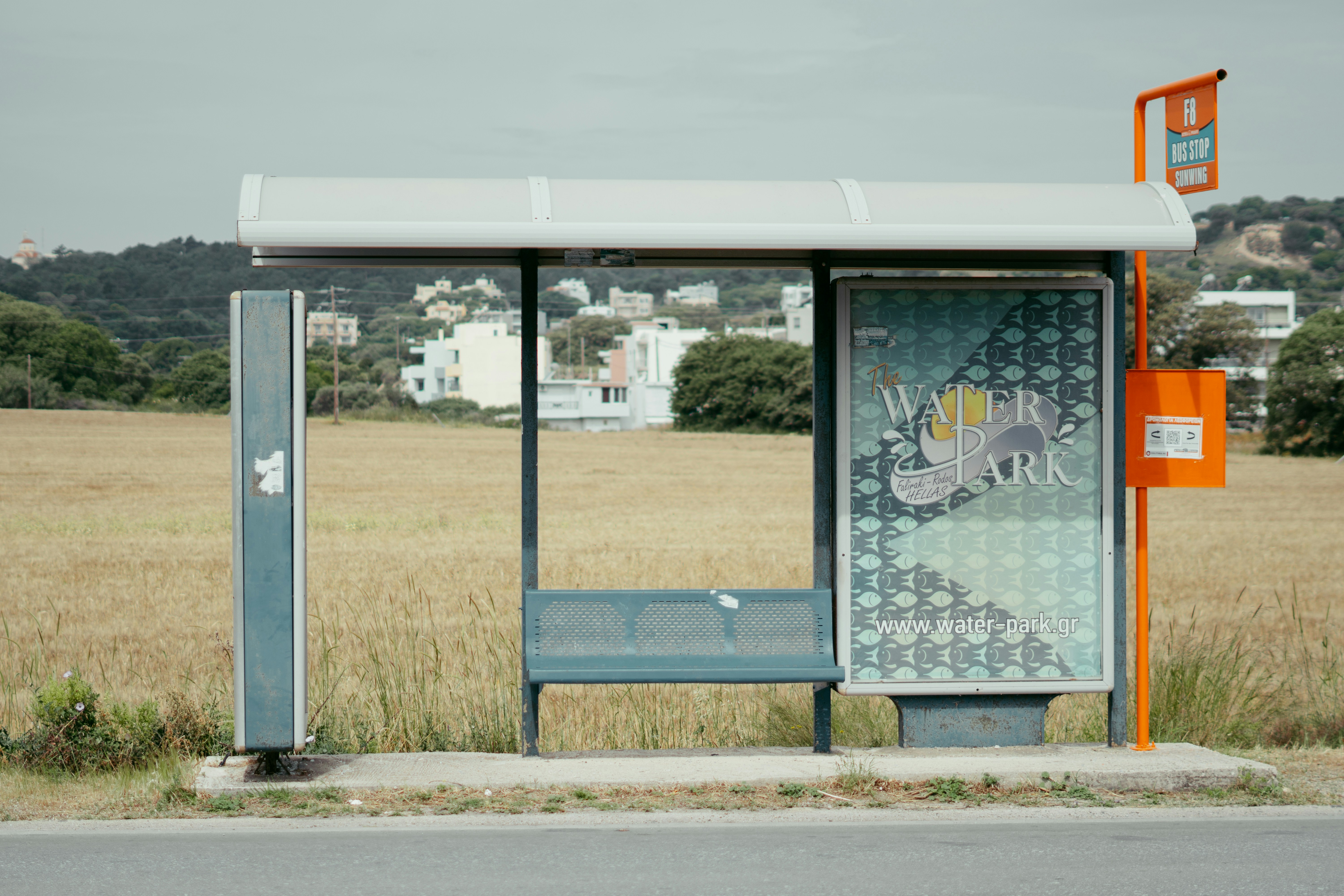 Bus stop featuring a Water Park advertisement, set against a backdrop of rolling hills and distant buildings. The scene conveys a tranquil moment in an urban environment.