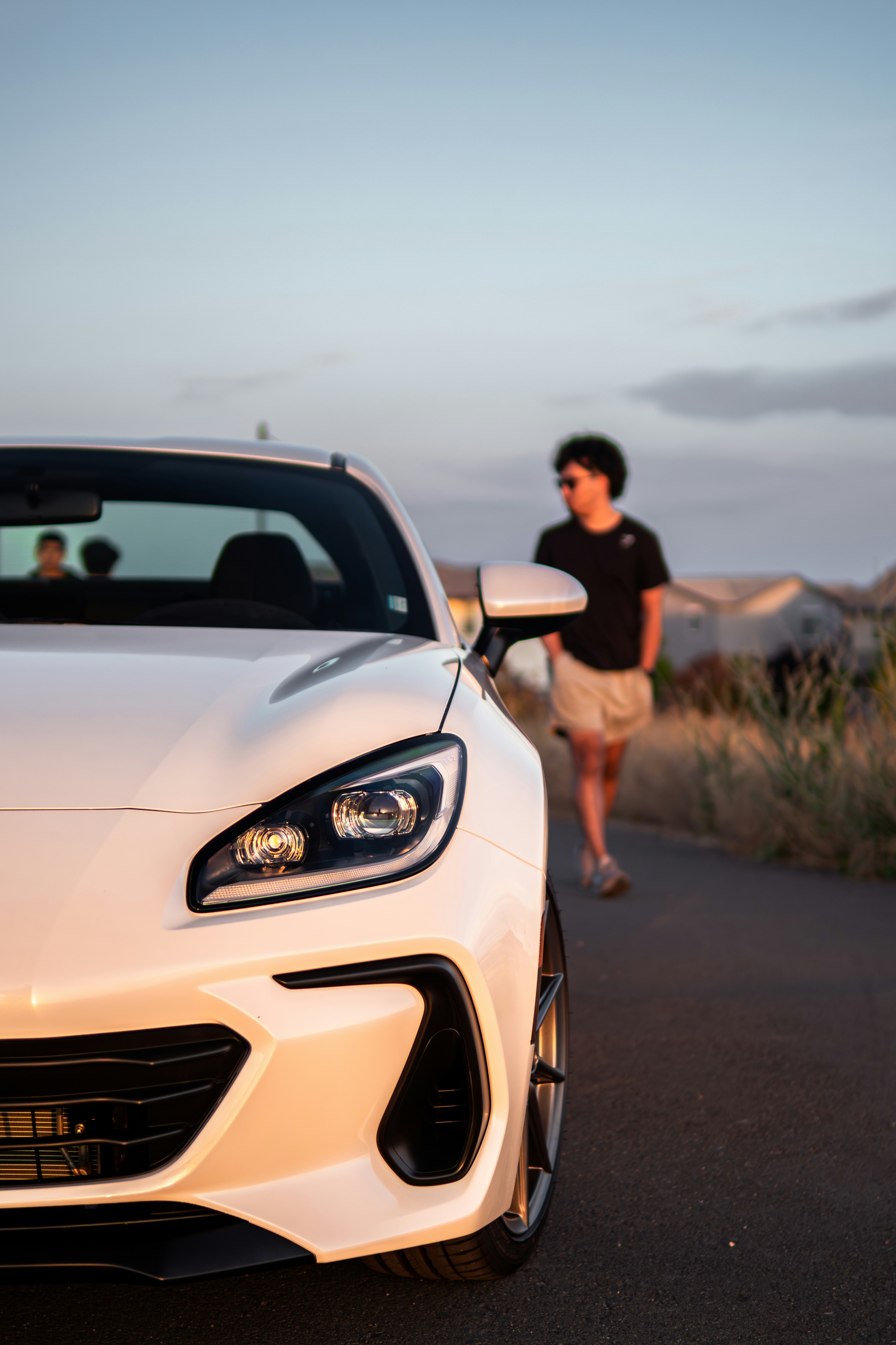 White sports car on a coastal road with a man strolling in the background