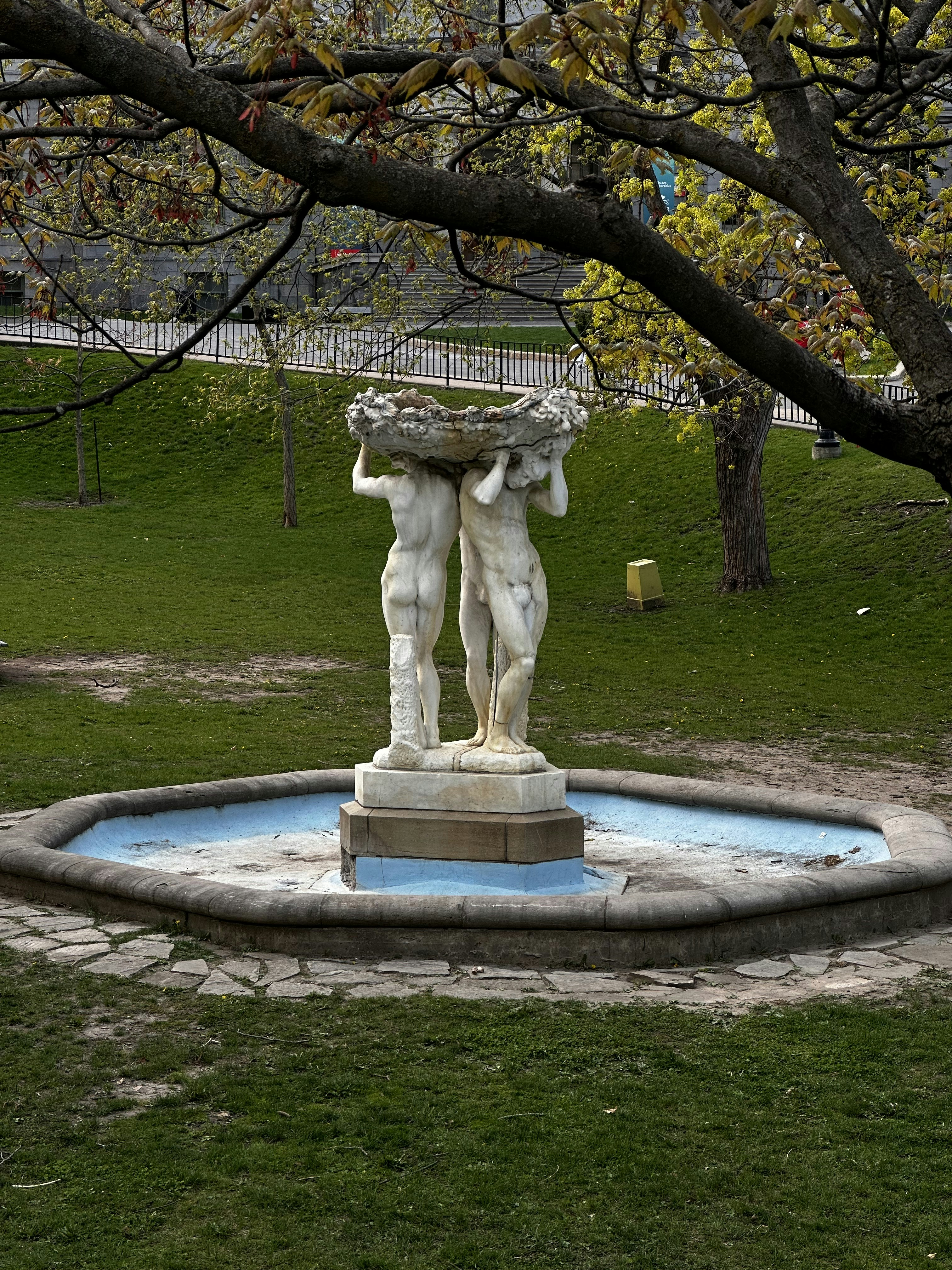 Stone Bearers Under Autumn Canopy: A Park Fountain Statue Duo