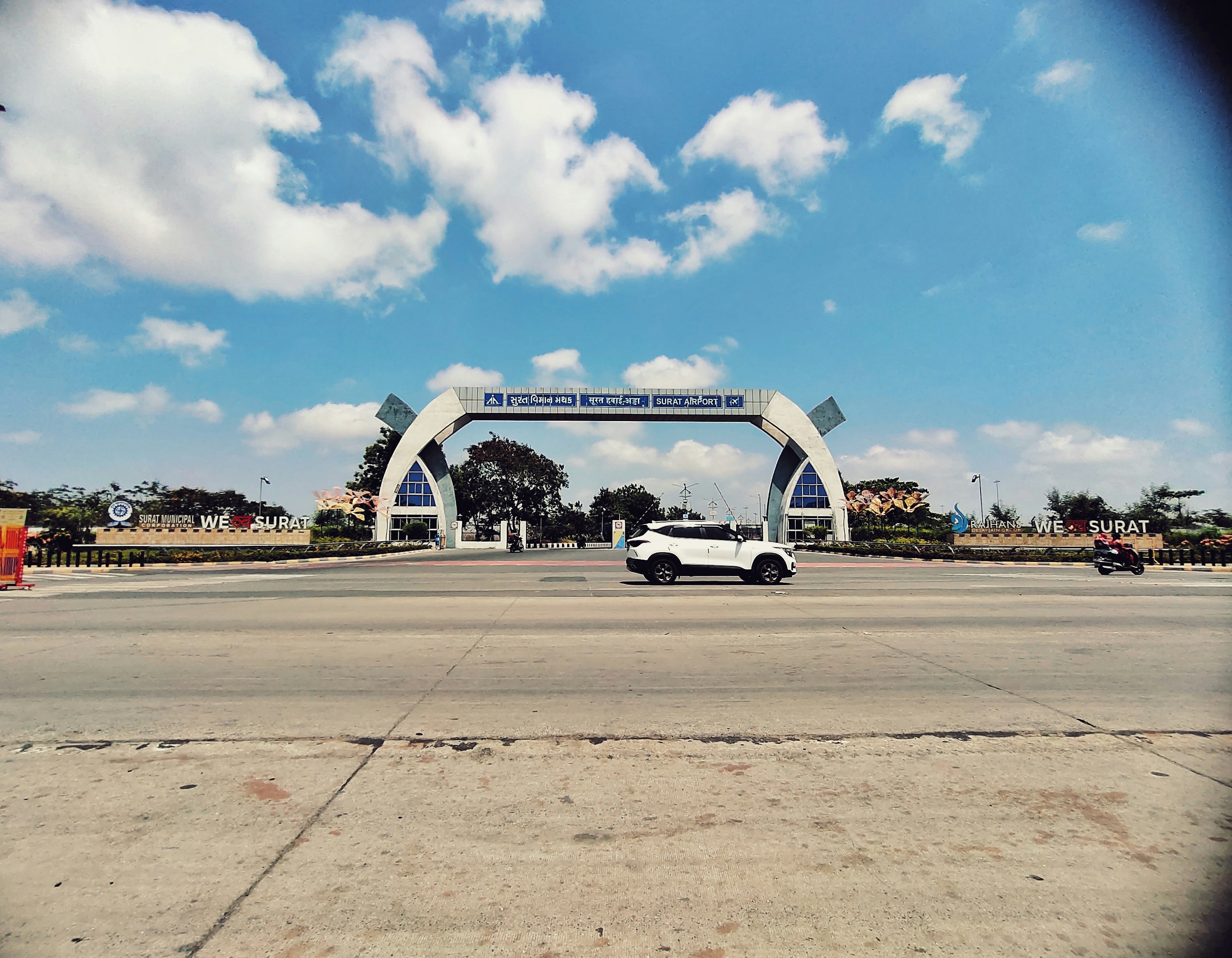 Arched structure with modern design spanning a wide road under a partly cloudy sky.