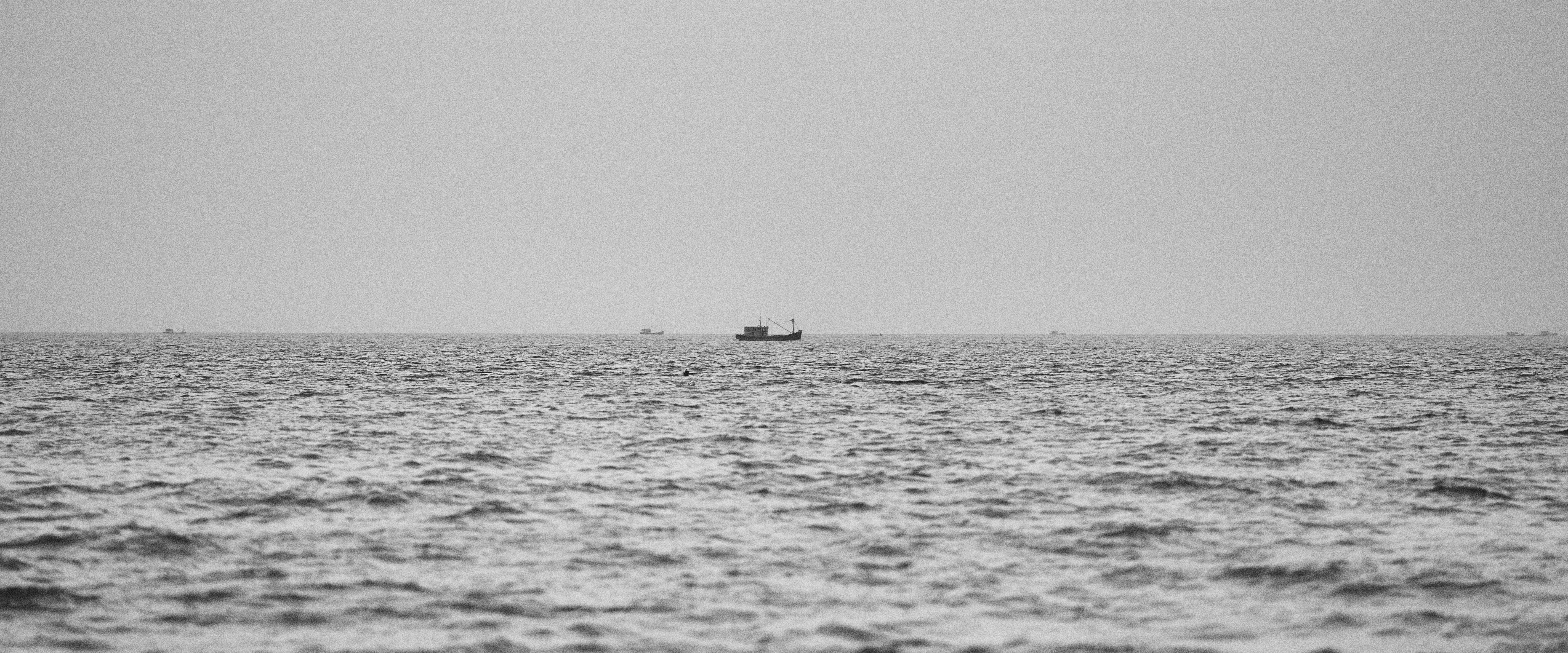 Distant boat on a calm, textured ocean under a cloudy sky.