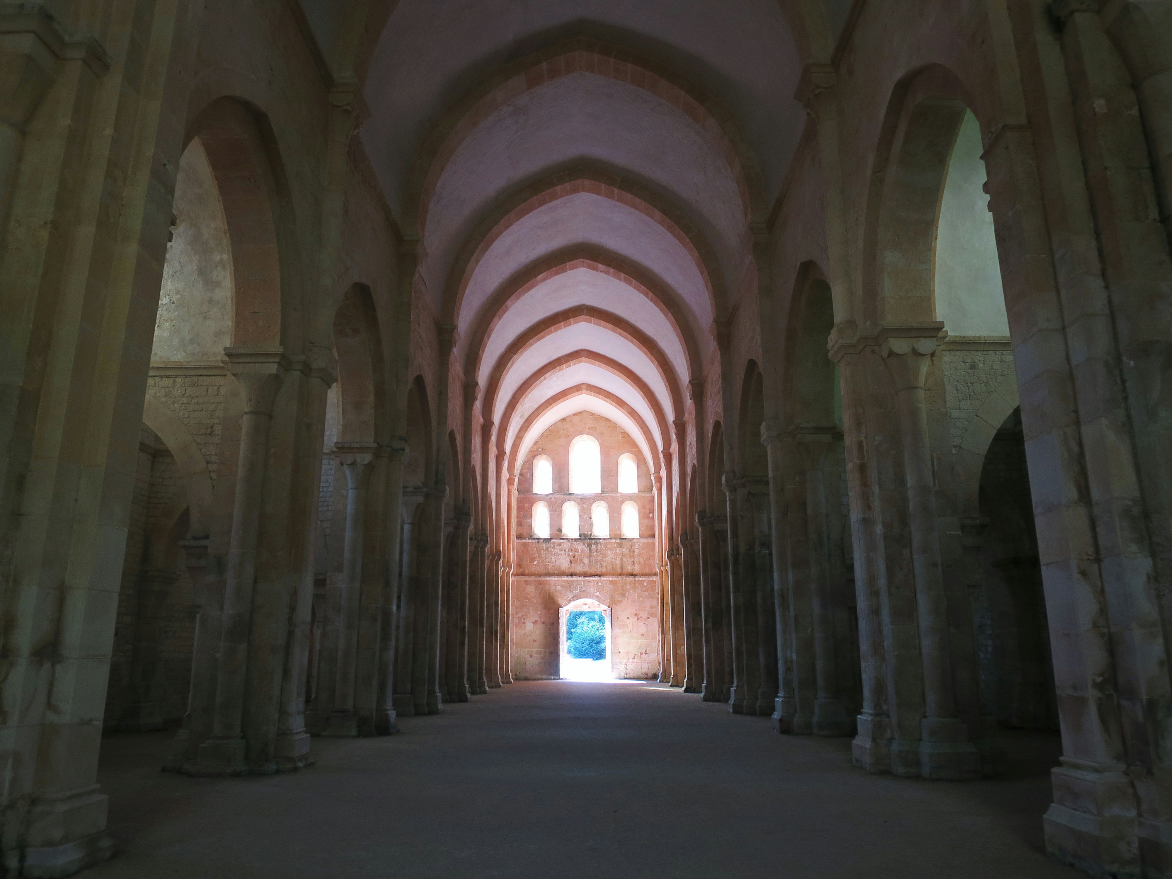Long Romanesque nave with repeating arches and stone columns, drawing the eye toward a bright doorway at the end.