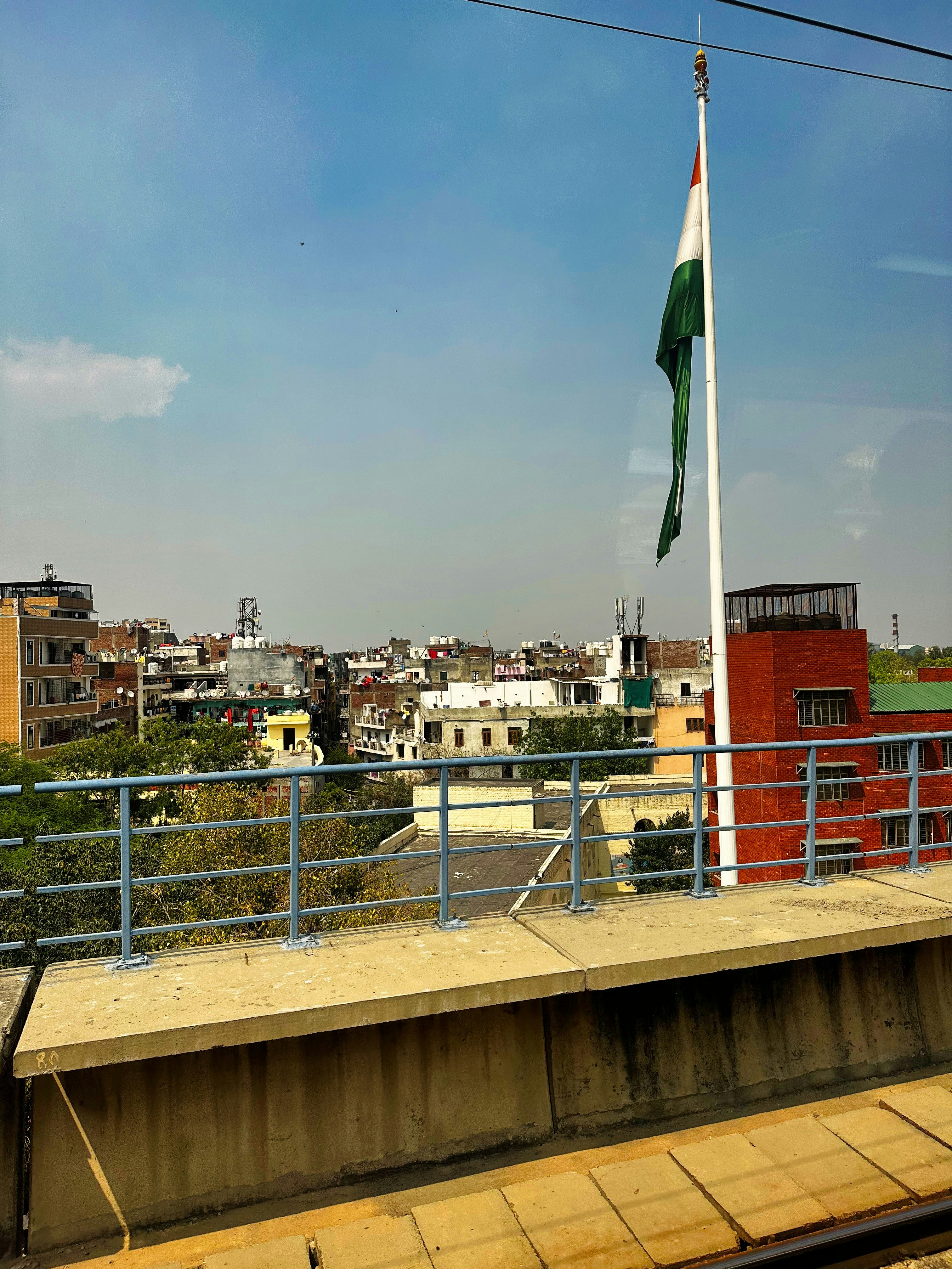 Flagpole Over a Sunlit City: Rooftop View into a Dense Indian Skyline