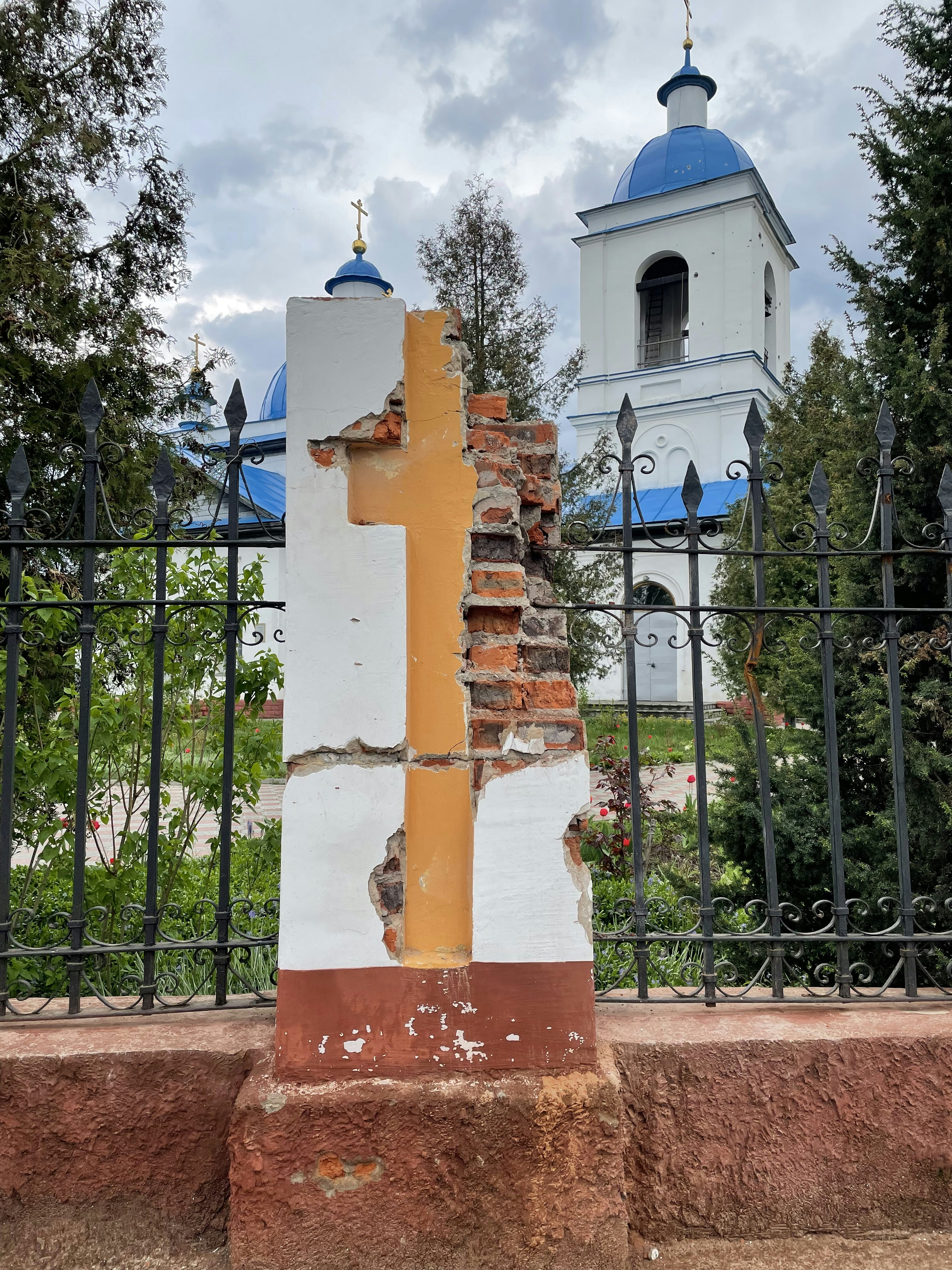 Ochre-White Ruin Framing a Blue-Domed Church Behind Iron Fence