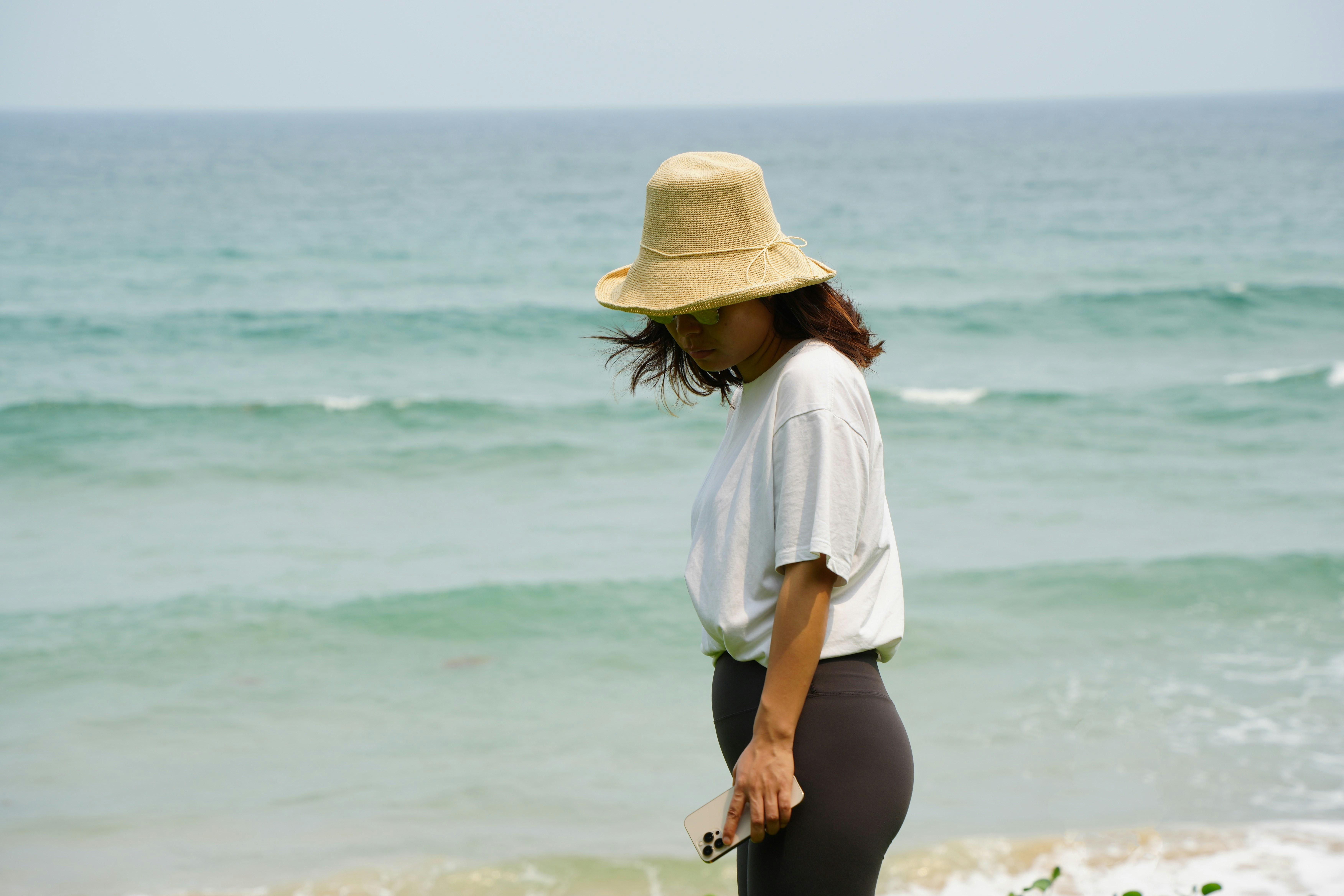 Beachside Quiet: A Woman in a Hat Kneels at the Waterline