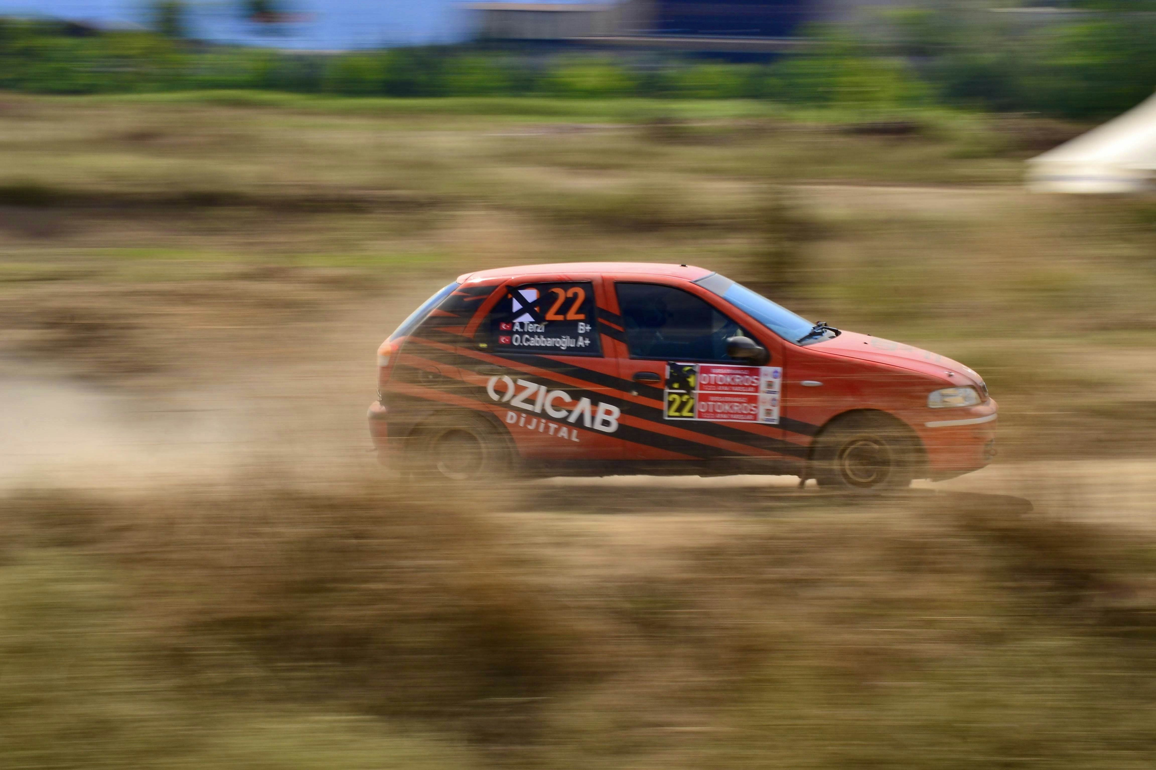 Red rally car speeding through a dirt track, surrounded by blurred motion and dust clouds.