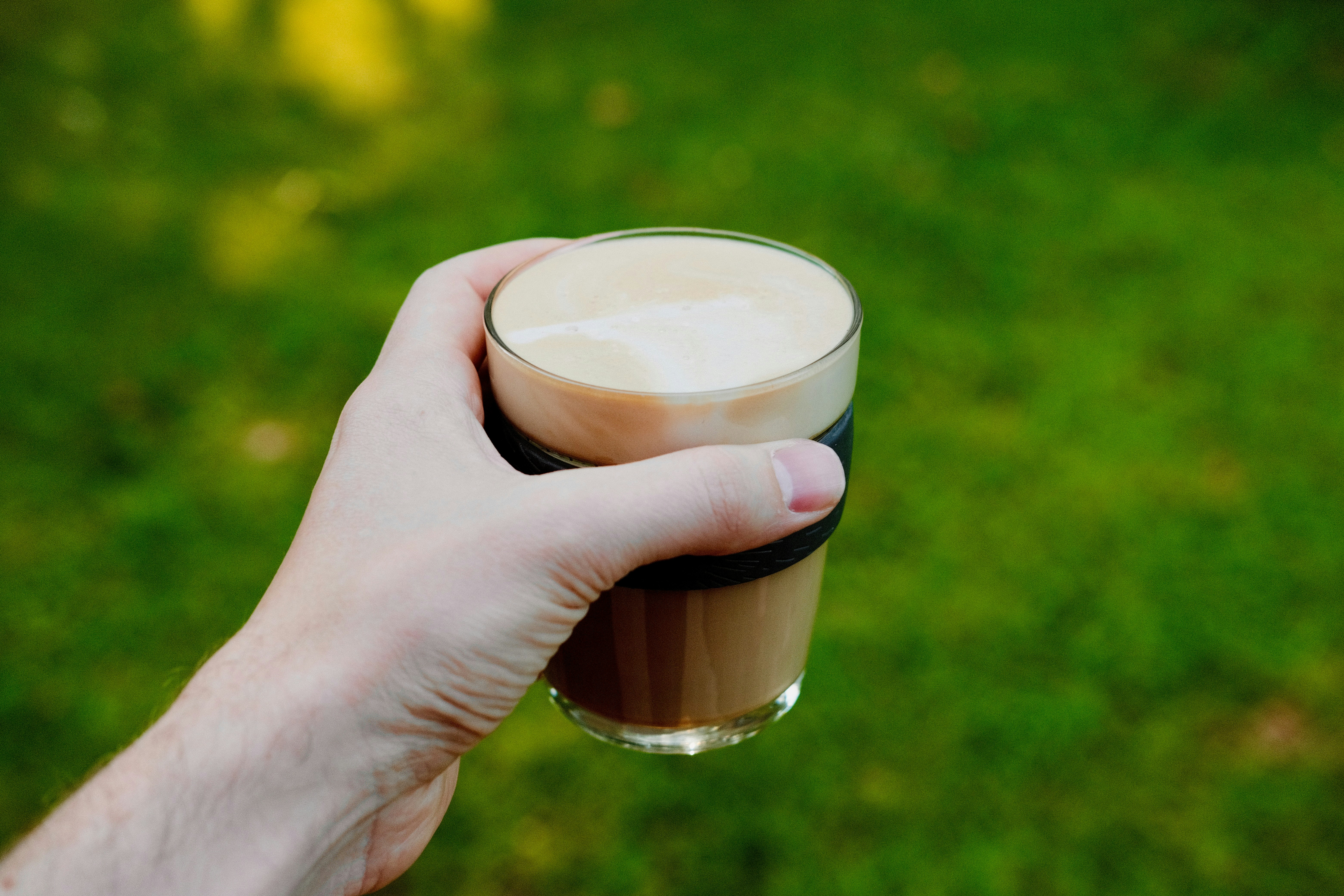 Foam on a Sunlit Lawn: Hand-Held Coffee Against Green Blur