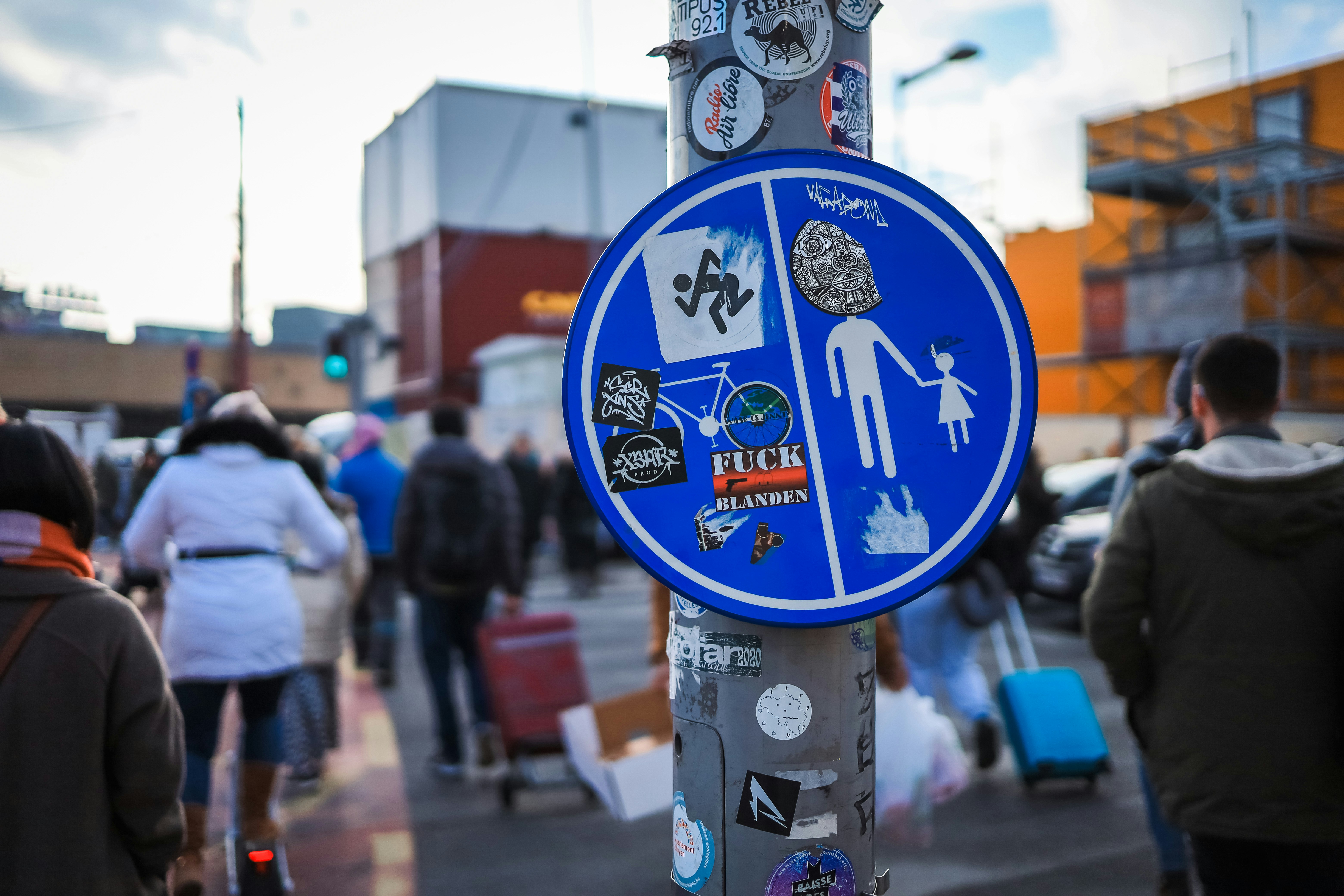 Stickered Blue Circle Sign Anchoring a Lively City Street