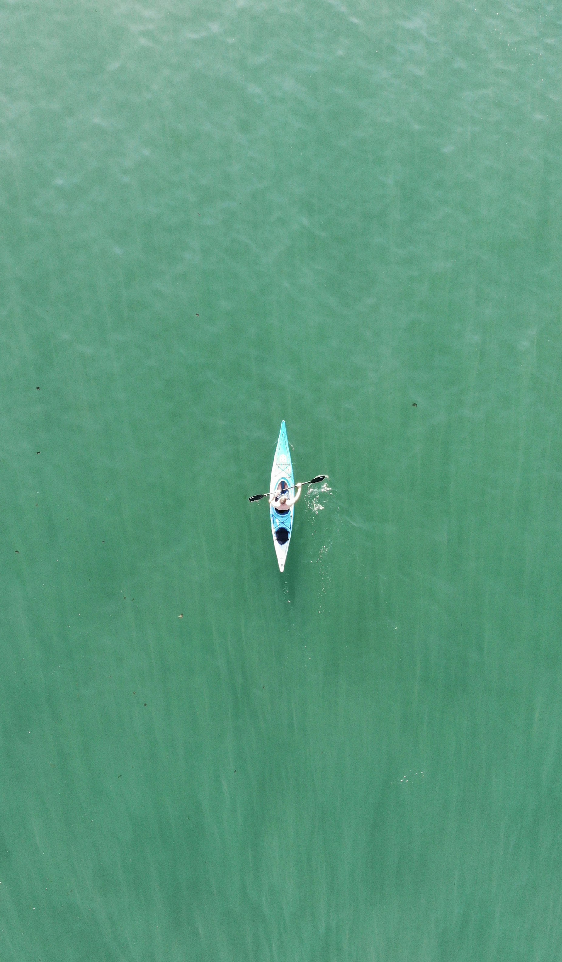 Emerald Quiet: A Solo Kayak Drifts Across a Glassy Green Sea