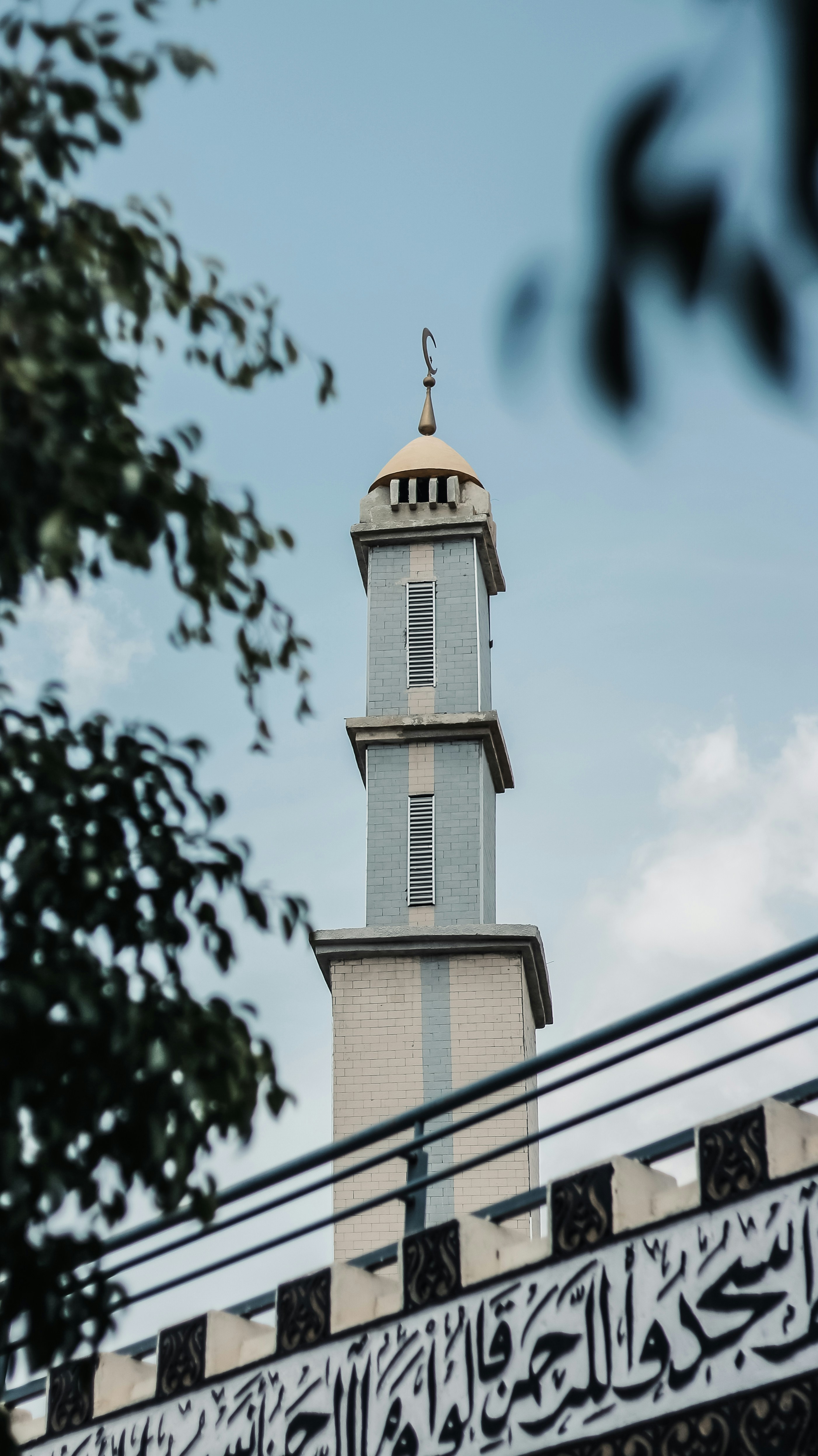 Copper-Domed Minaret Soars Over An Ornate Arabic Frieze Under a Clear Sky