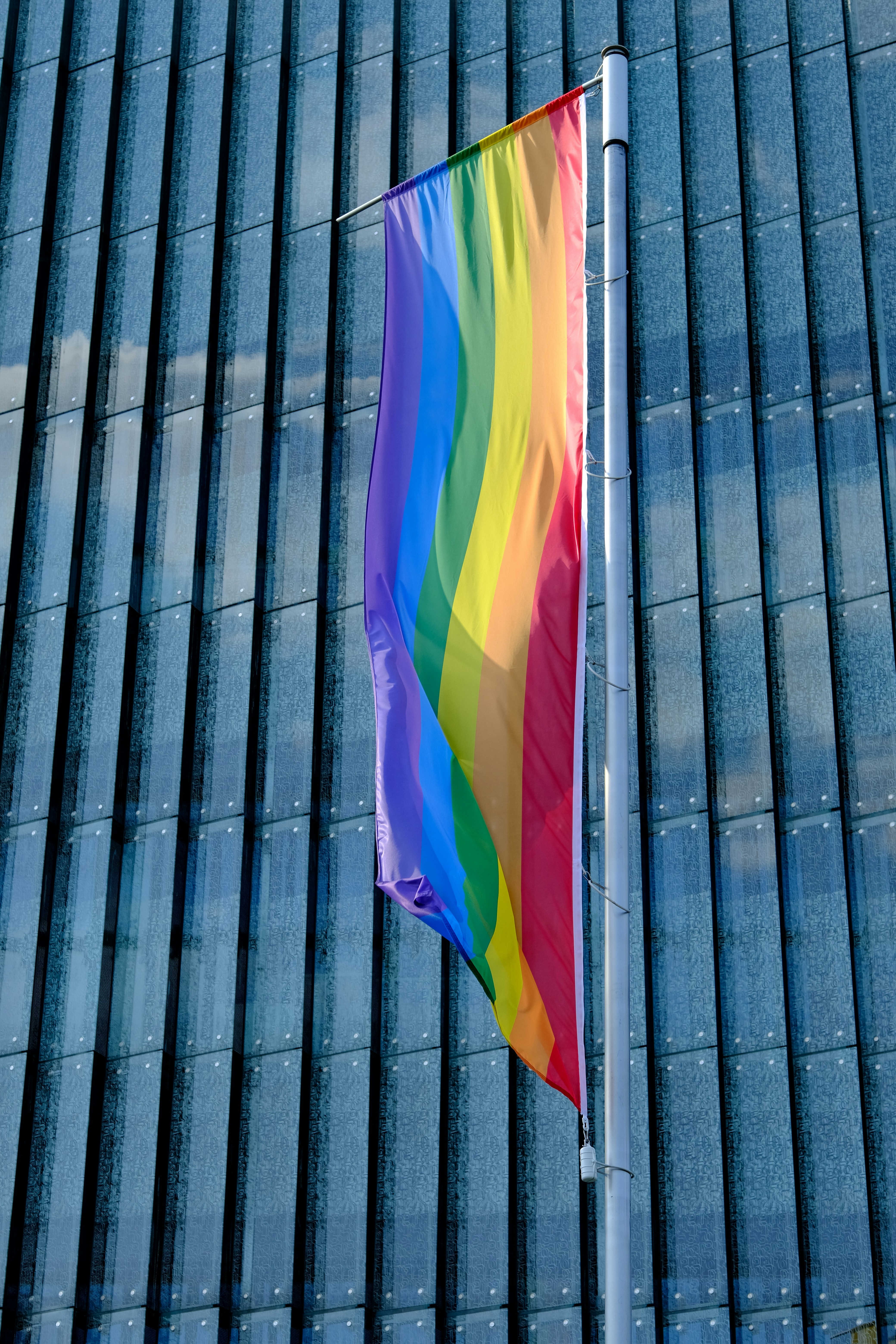Vertical Rainbow Flag Framed by a Faceted Glass Façade