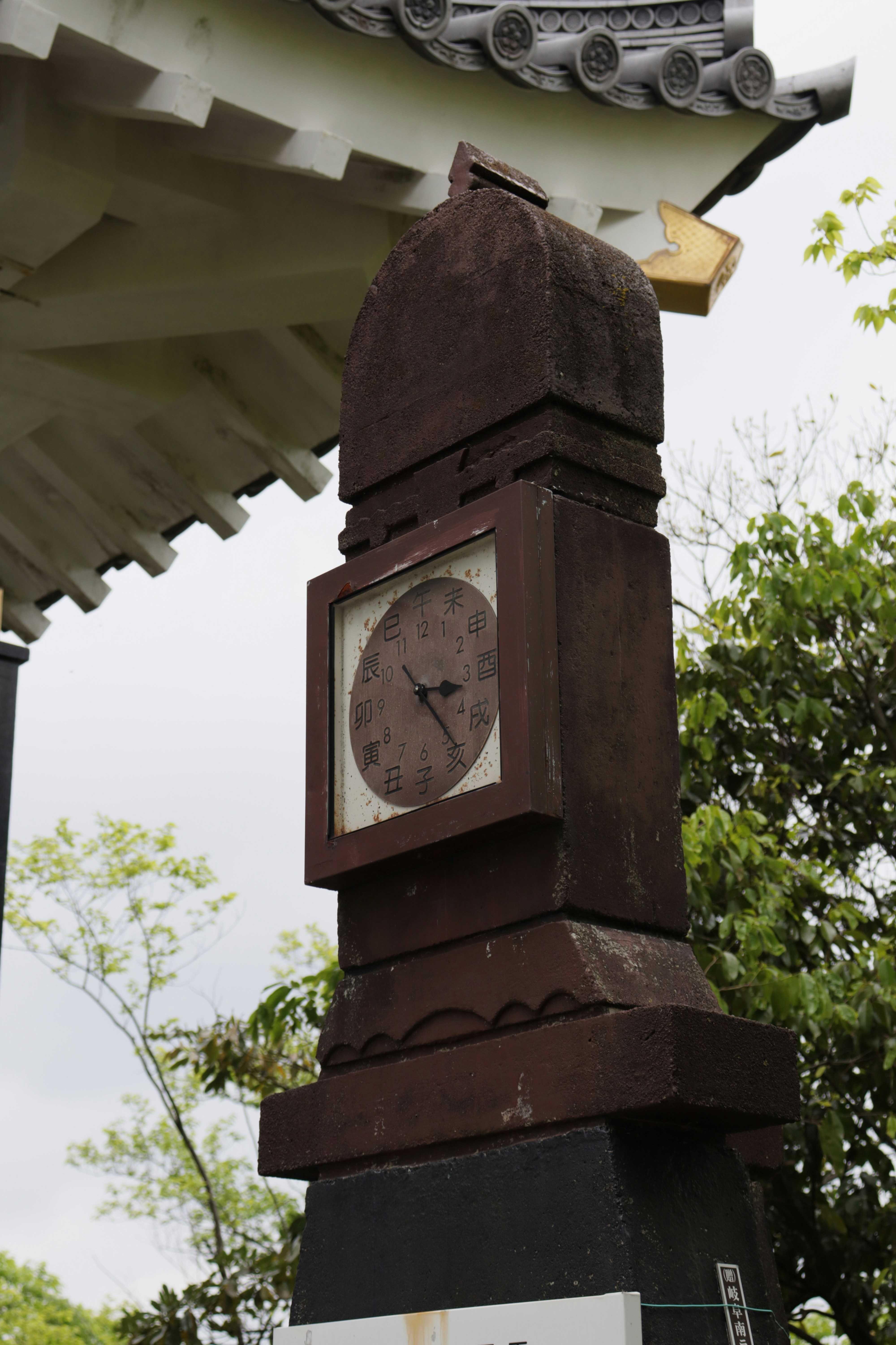Weathered Clock on Stone Pillar Beneath Temple Eaves