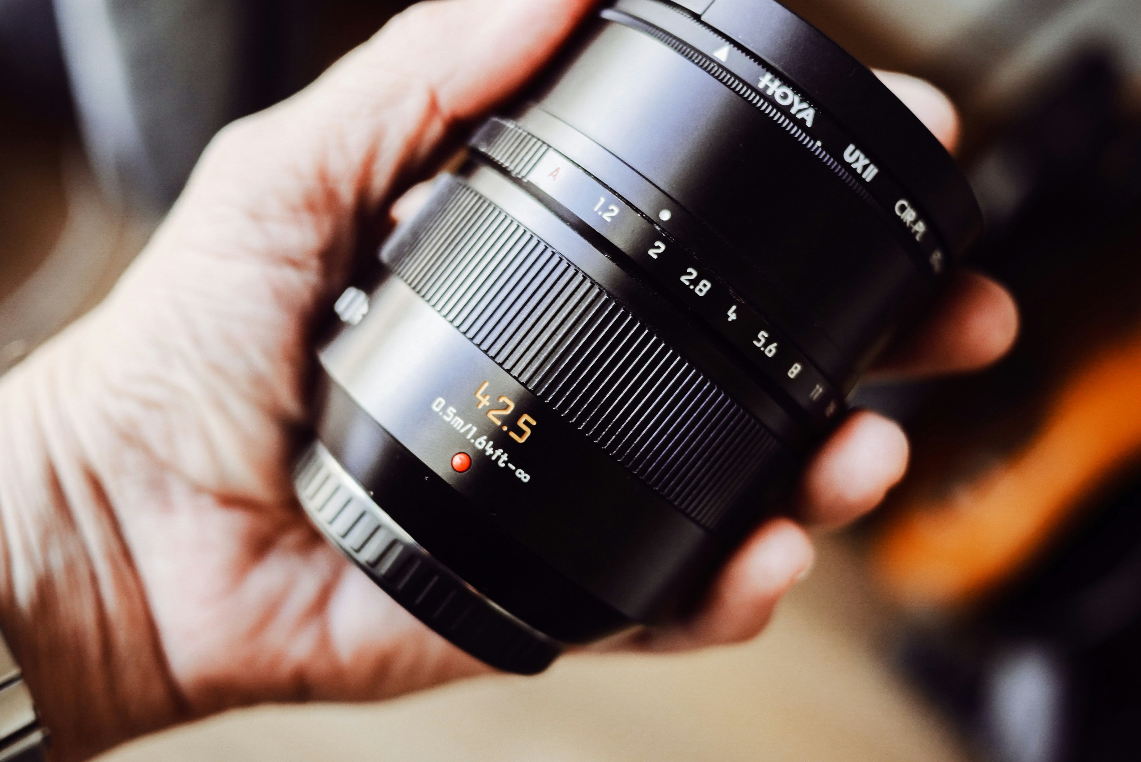 Hand holding a Panasonic Lumix lens with visible aperture settings.