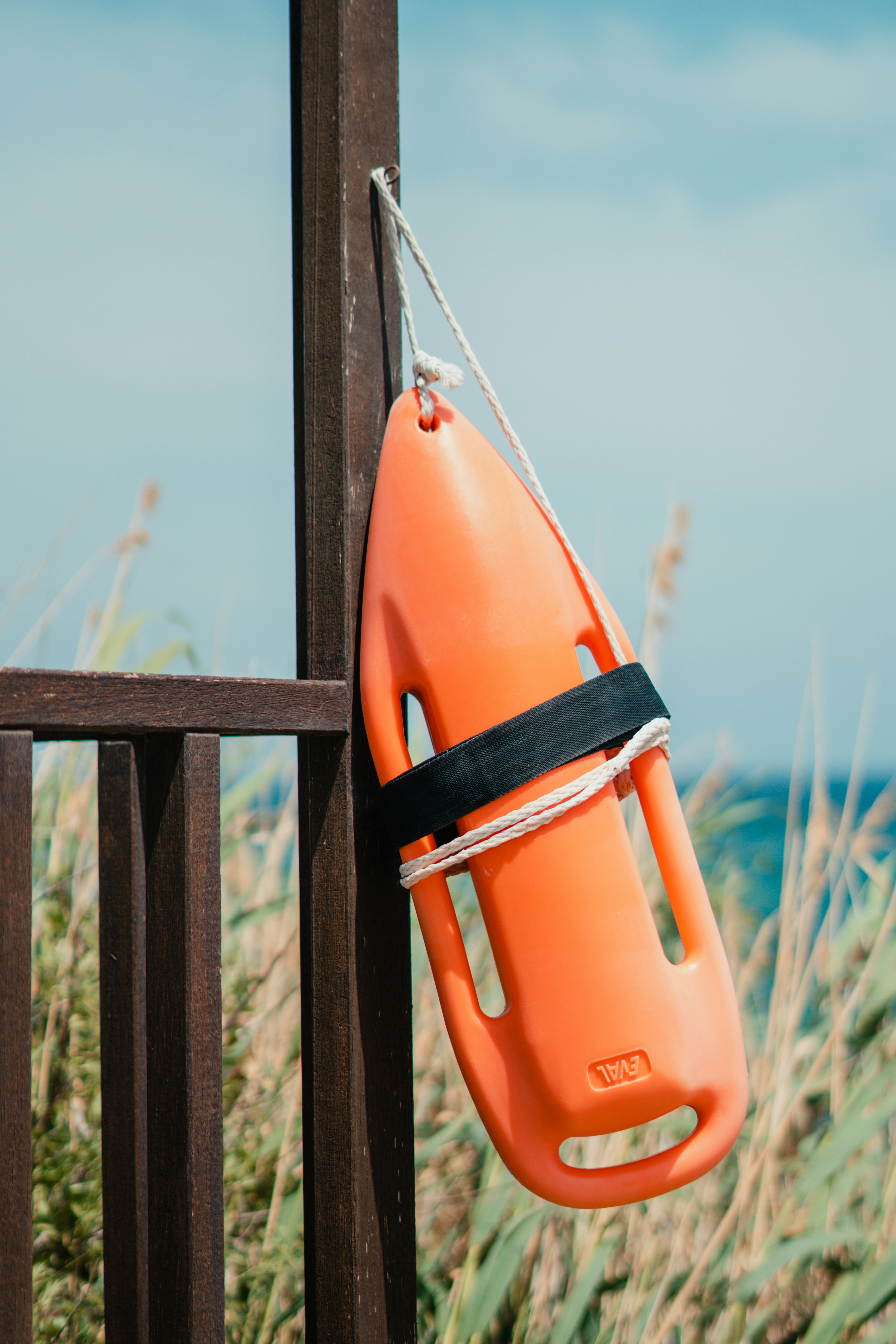Seaside Lifebuoy: tethered orange rescue buoy on a weathered fence with sea breeze in the background