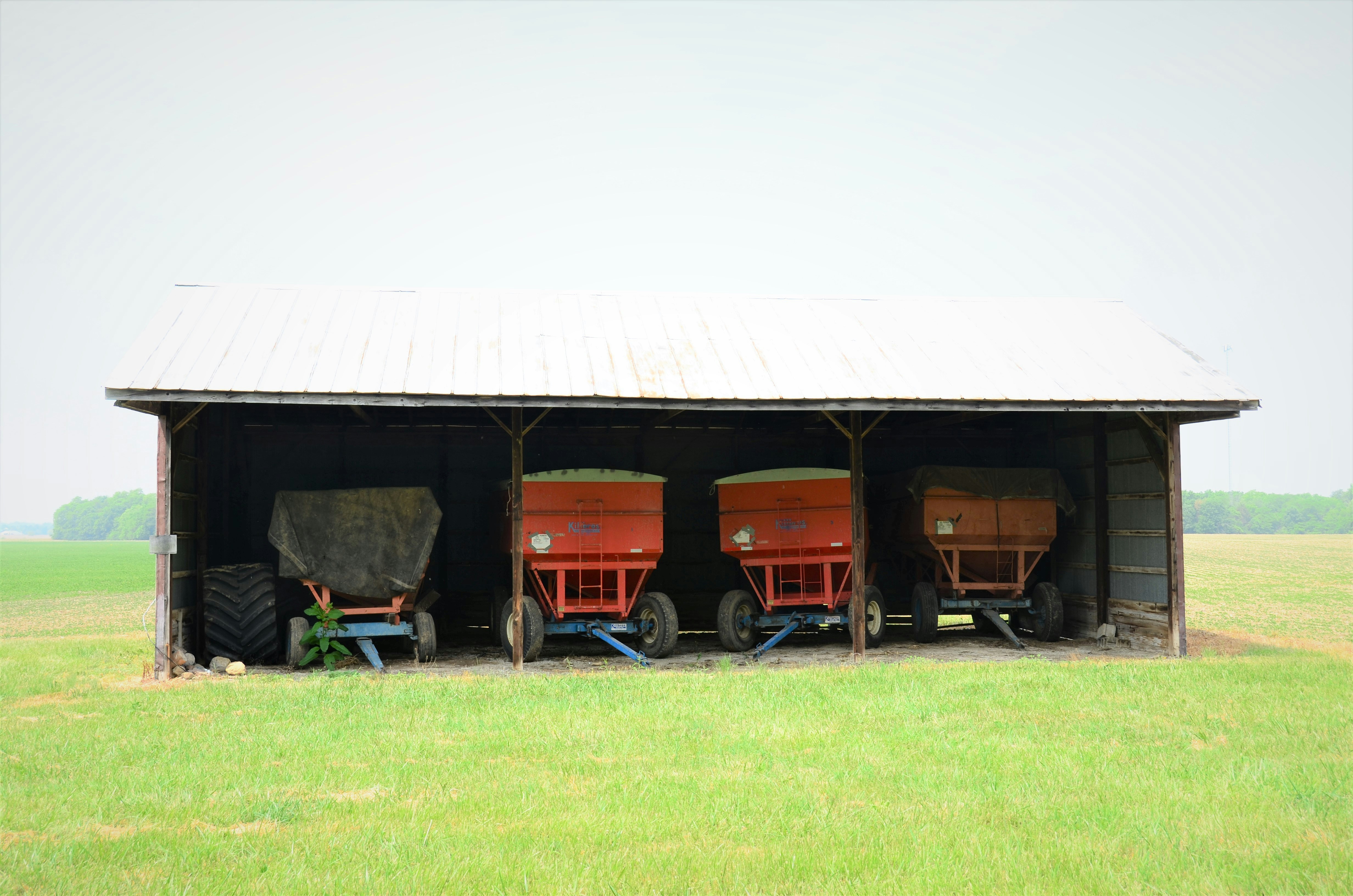 Three Red Tractors Rest Under a Weathered Shelter on a Quiet Prairie