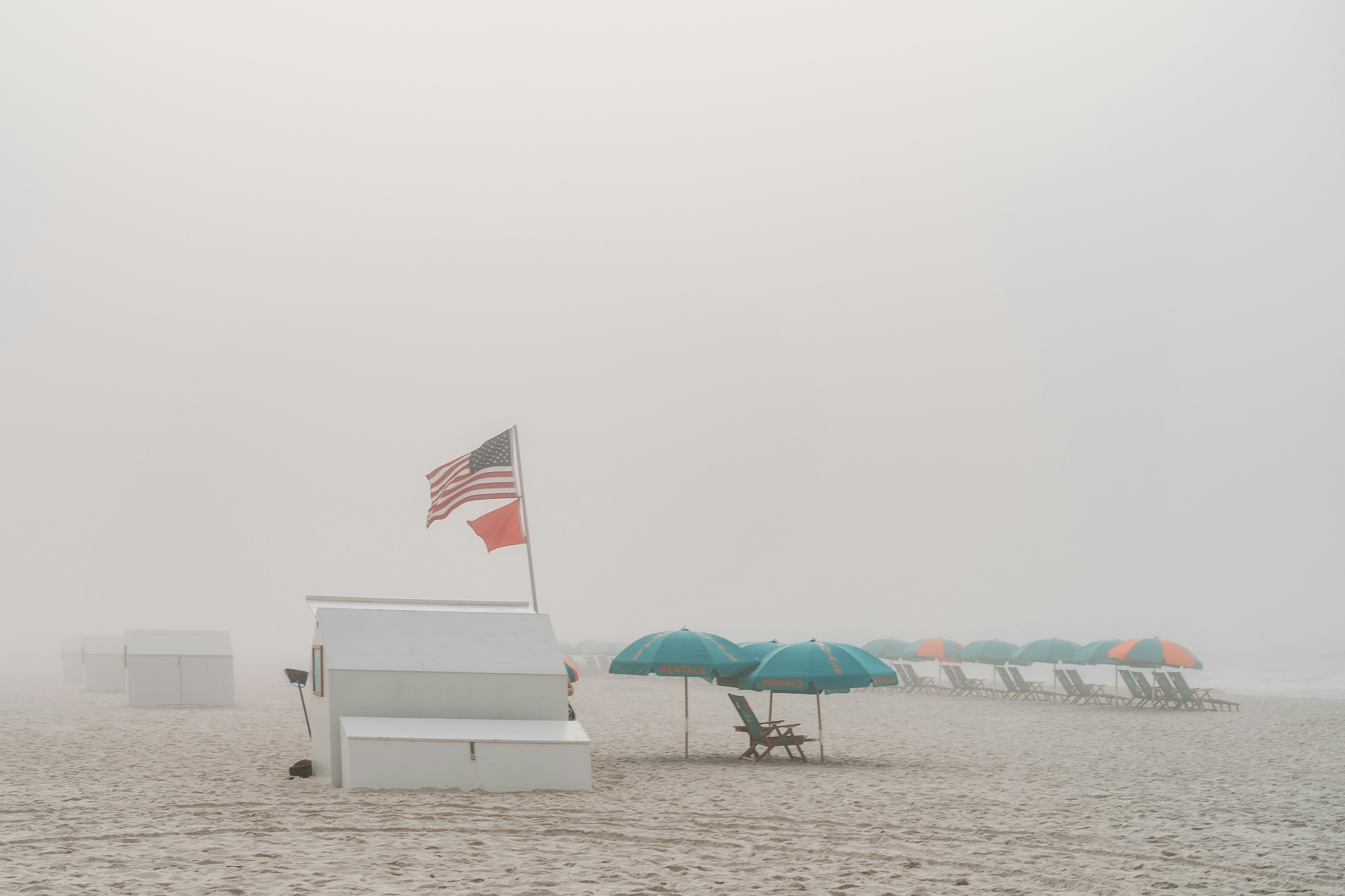 Fogbound Shoreline: A Lifeguard Chair and Flag Amid a Row of Umbrellas in Morning Mist