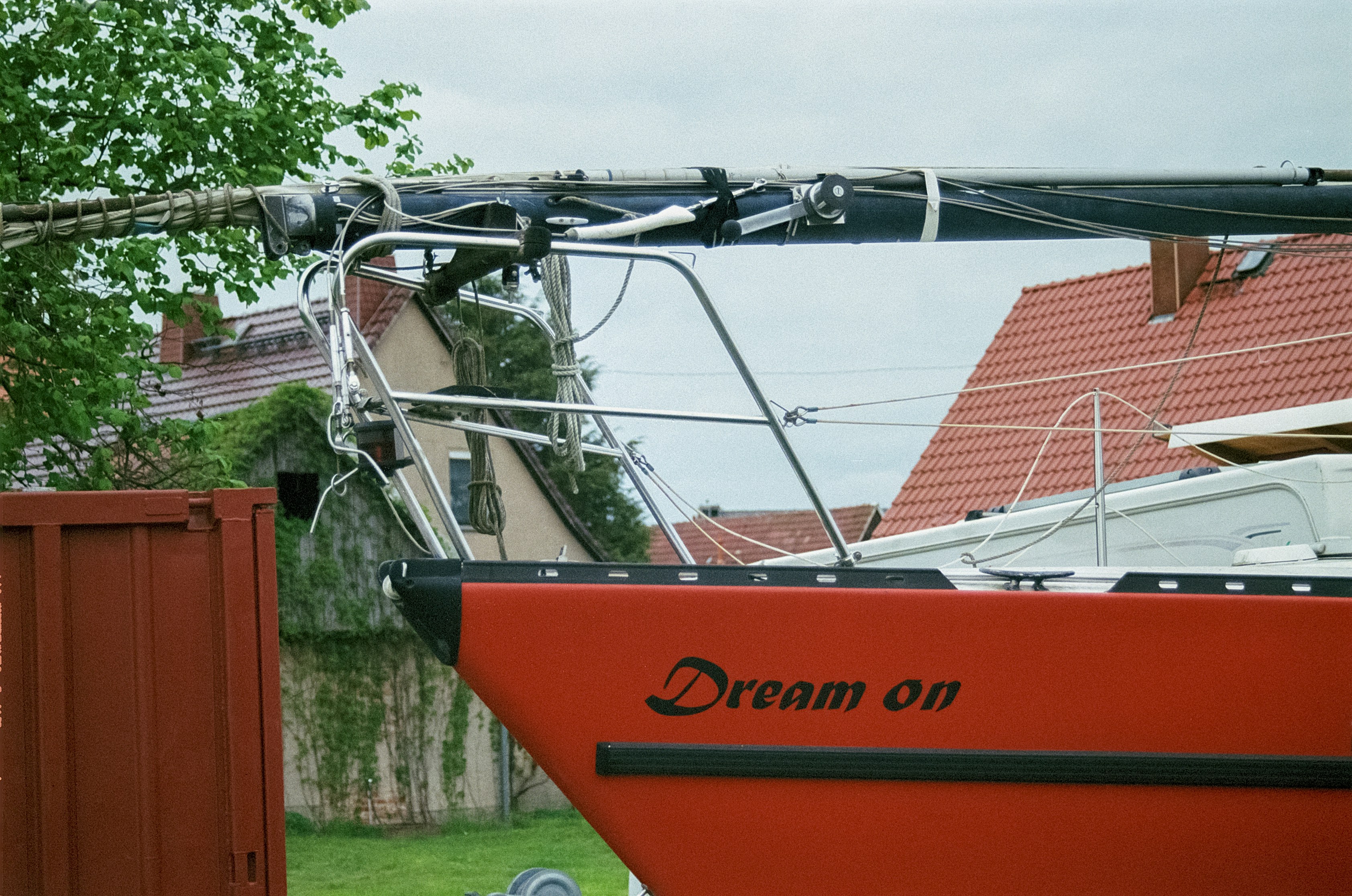 Dream On in a Quiet Yard: A Red Sailboat Between Green Lawn and Red Roofs