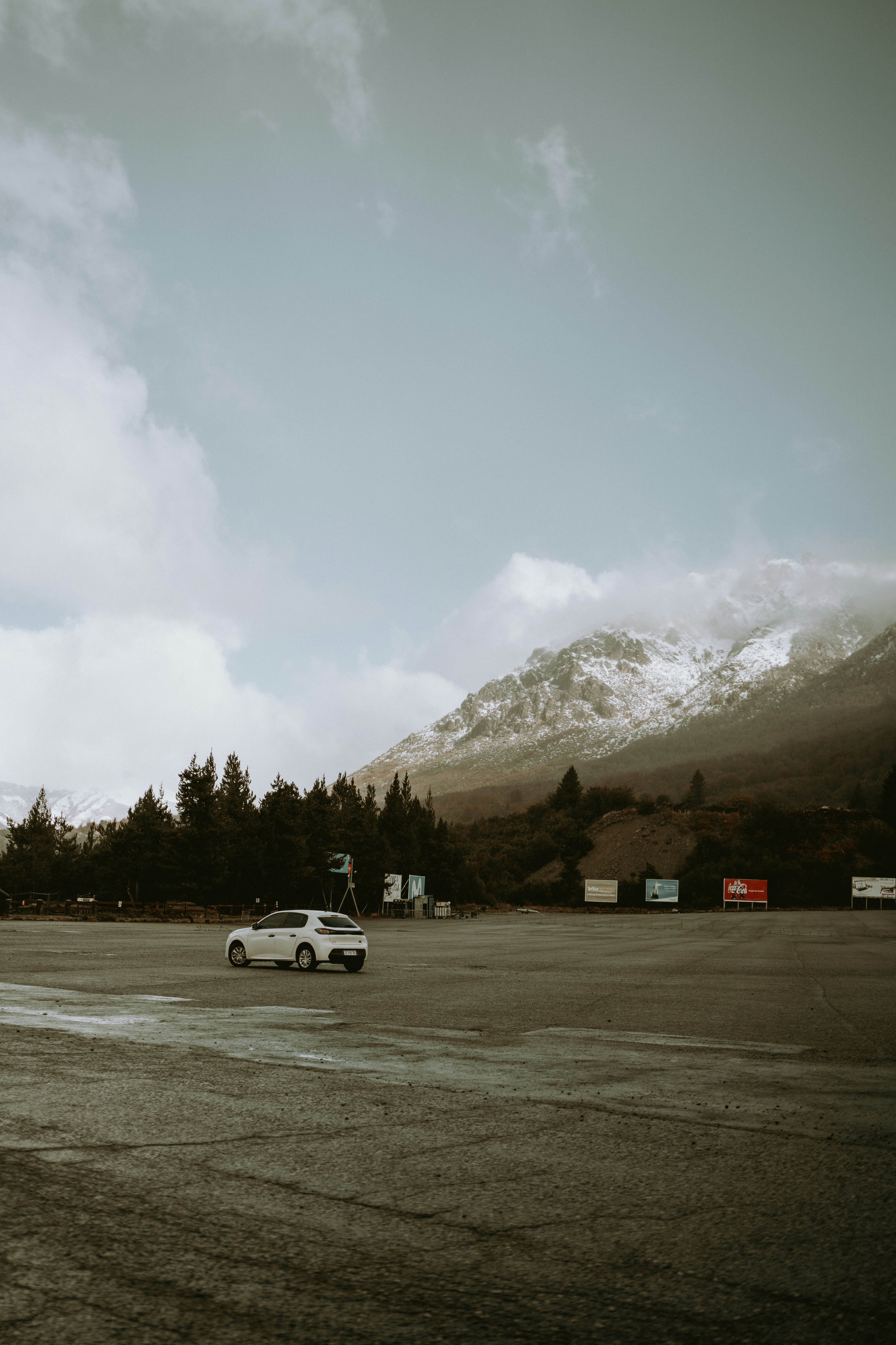White car parked on an expansive mountain lot with snow-capped peaks in the background.