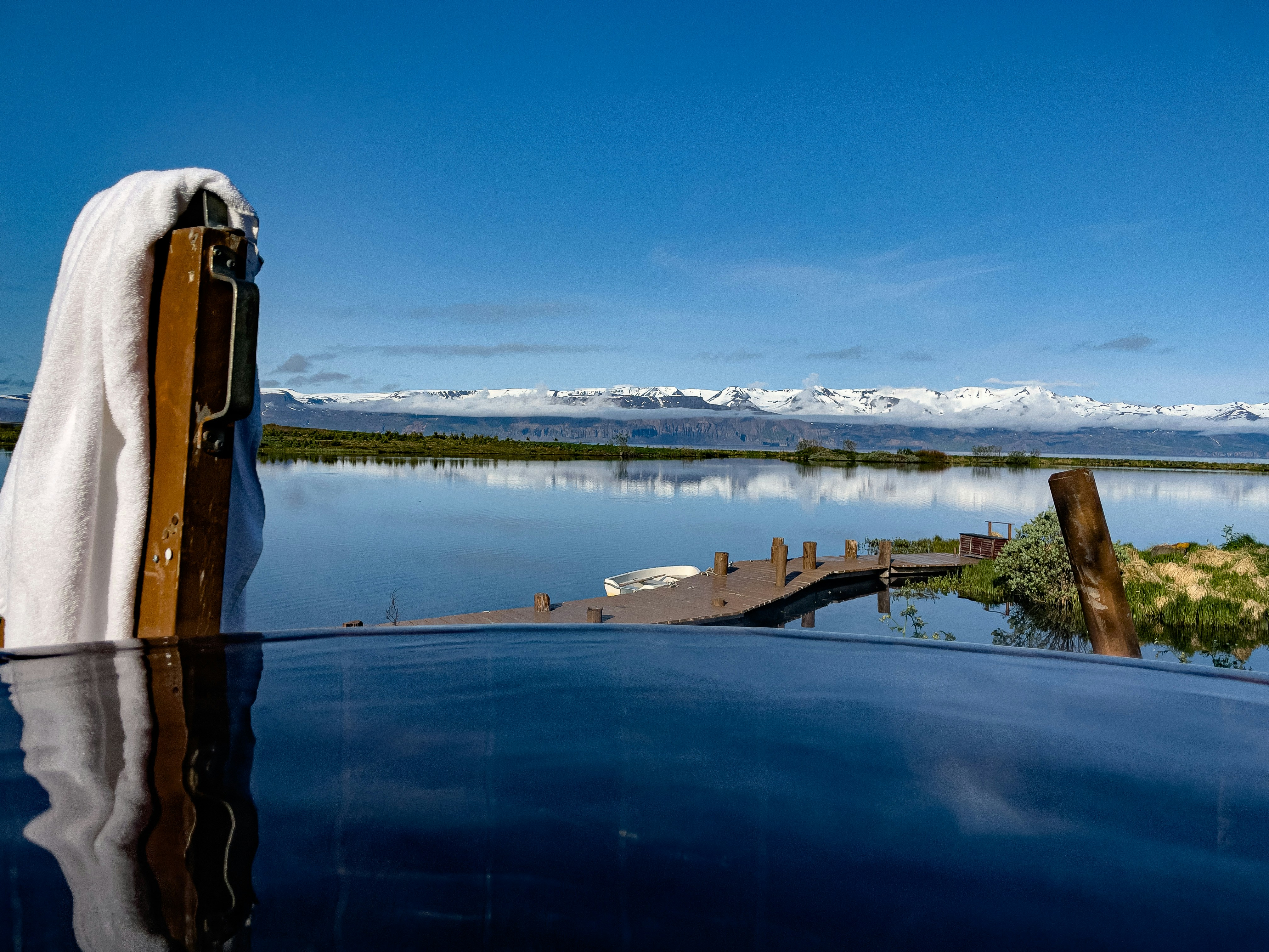 Hot tub overlooking a tranquil bay with distant snow-capped mountains under a clear blue sky.