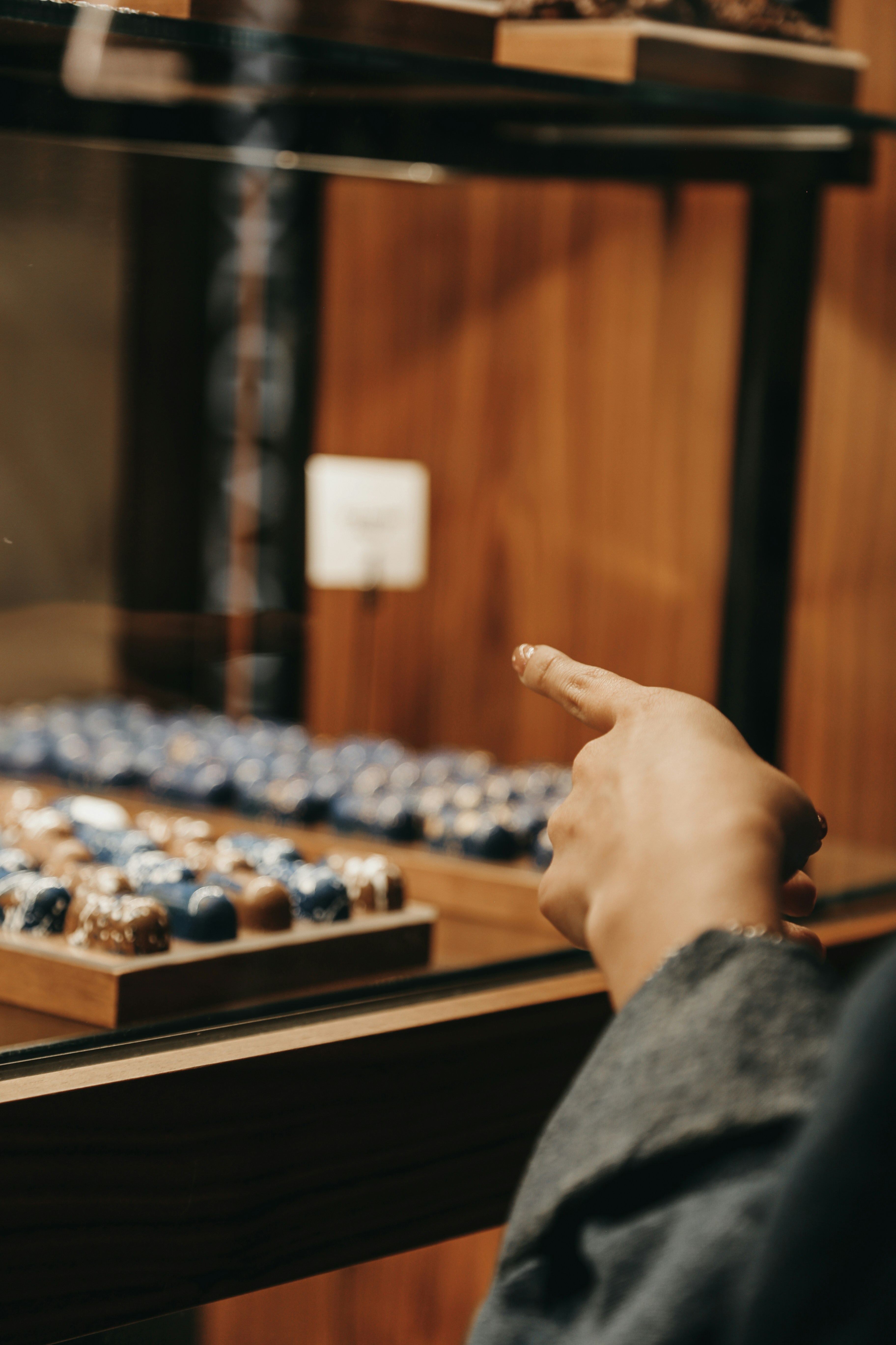 Hand Hovering Over a Row of Chocolates Behind Glass