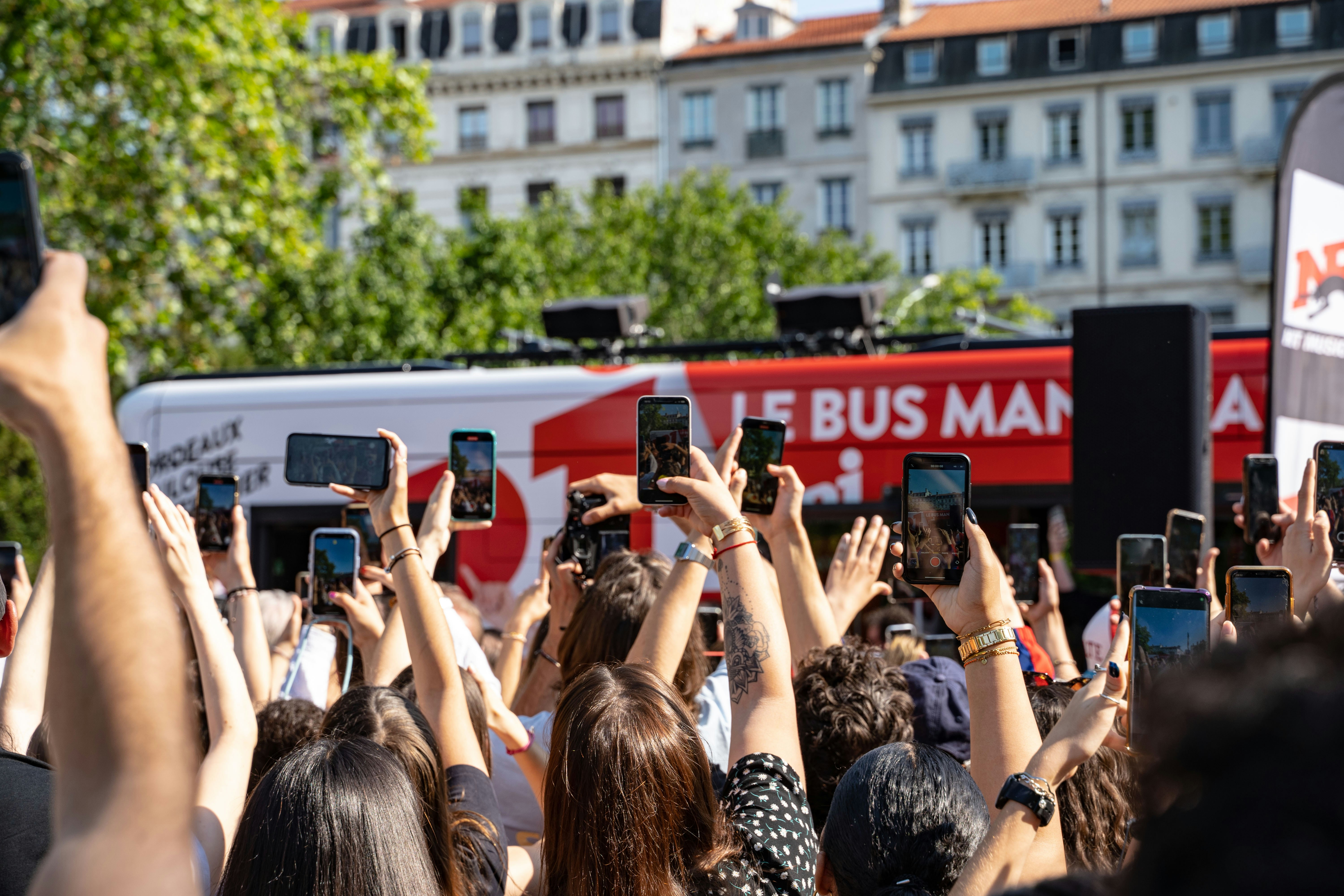 Crowd holding up smartphones capturing an event in front of a bus in Lyon's Place Carnot.