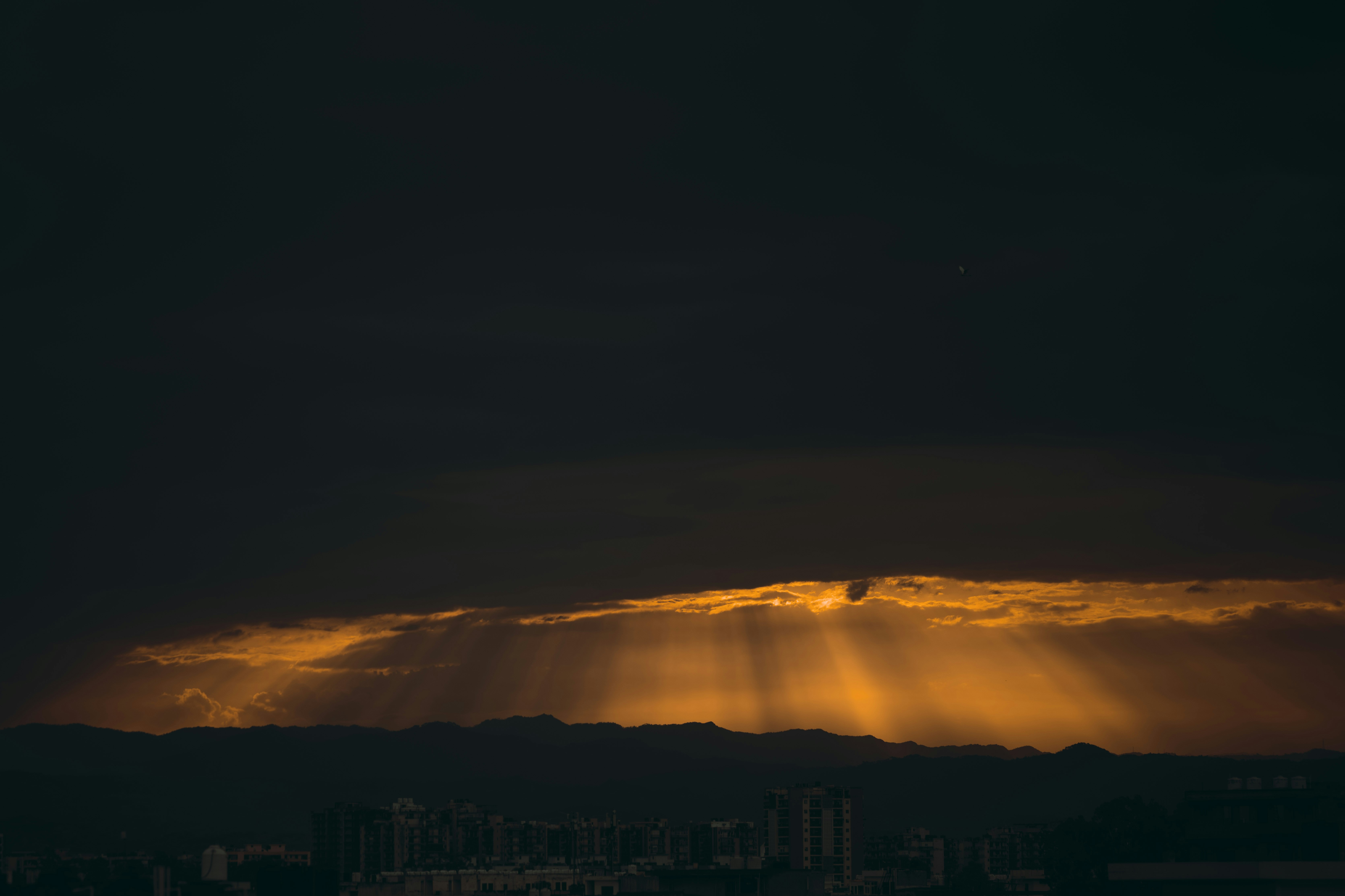 Sunbeams piercing through dark clouds above a city skyline at dusk.