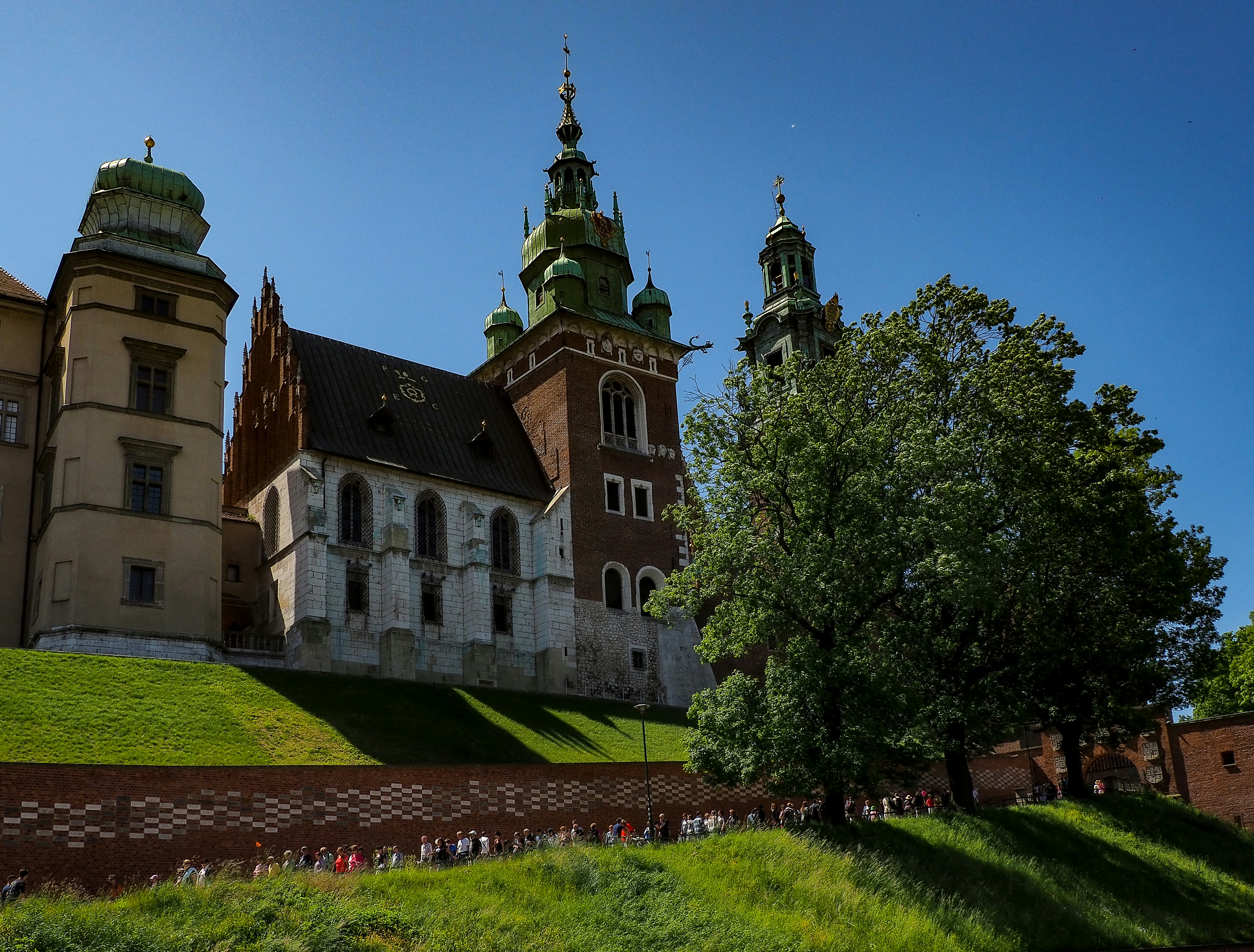 Historic castle with ornate towers set against a clear blue sky, framed by lush greenery.