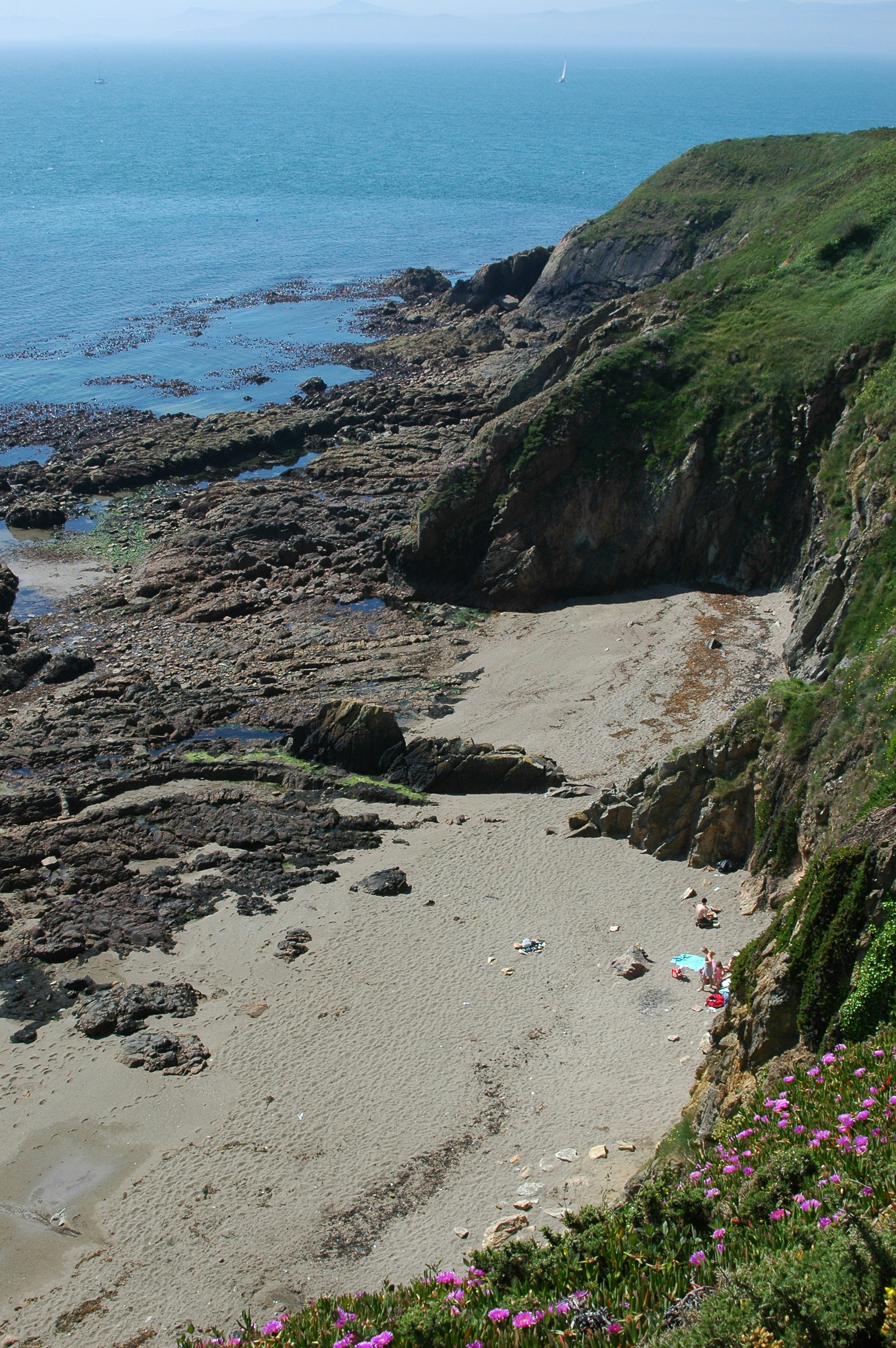 Cliffside Cove: Sunlit Beach Nestled Among Green Slopes