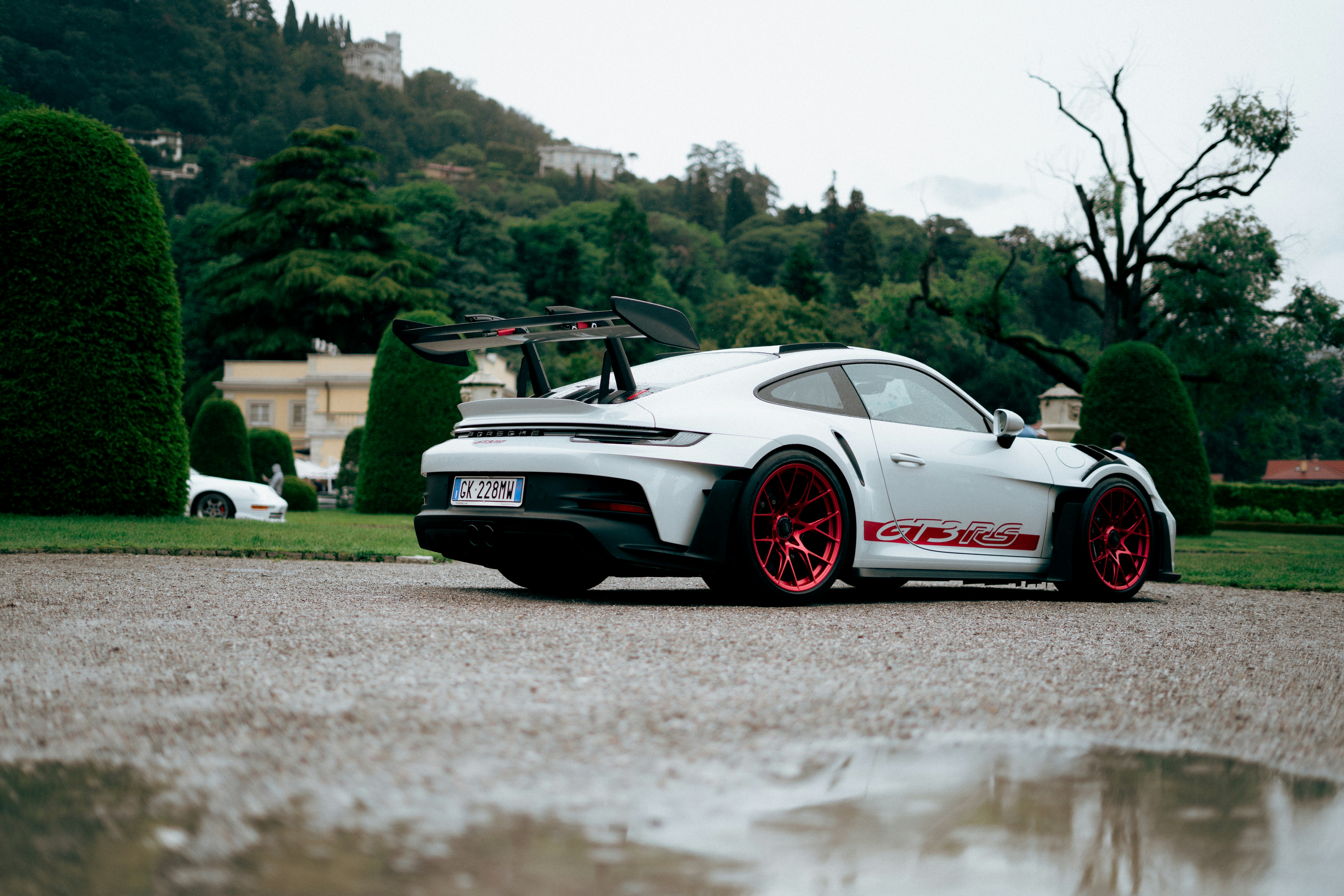 Racing Elegance: White Porsche with Bold Red Wheels on a Serene Estate