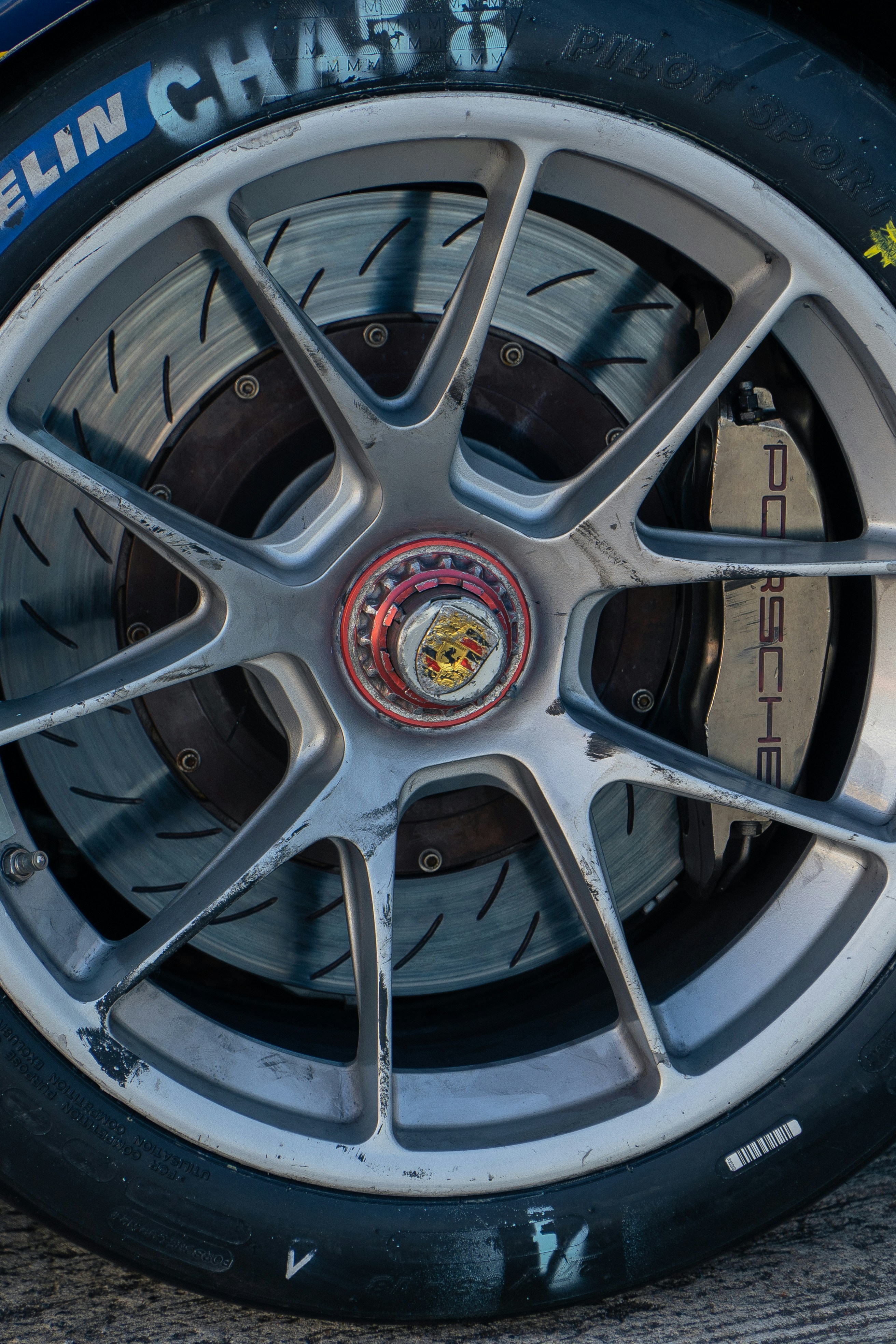 Red Crest at the Wheel's Core: A Porsche Rim Amid a Bluish Rotor Blur