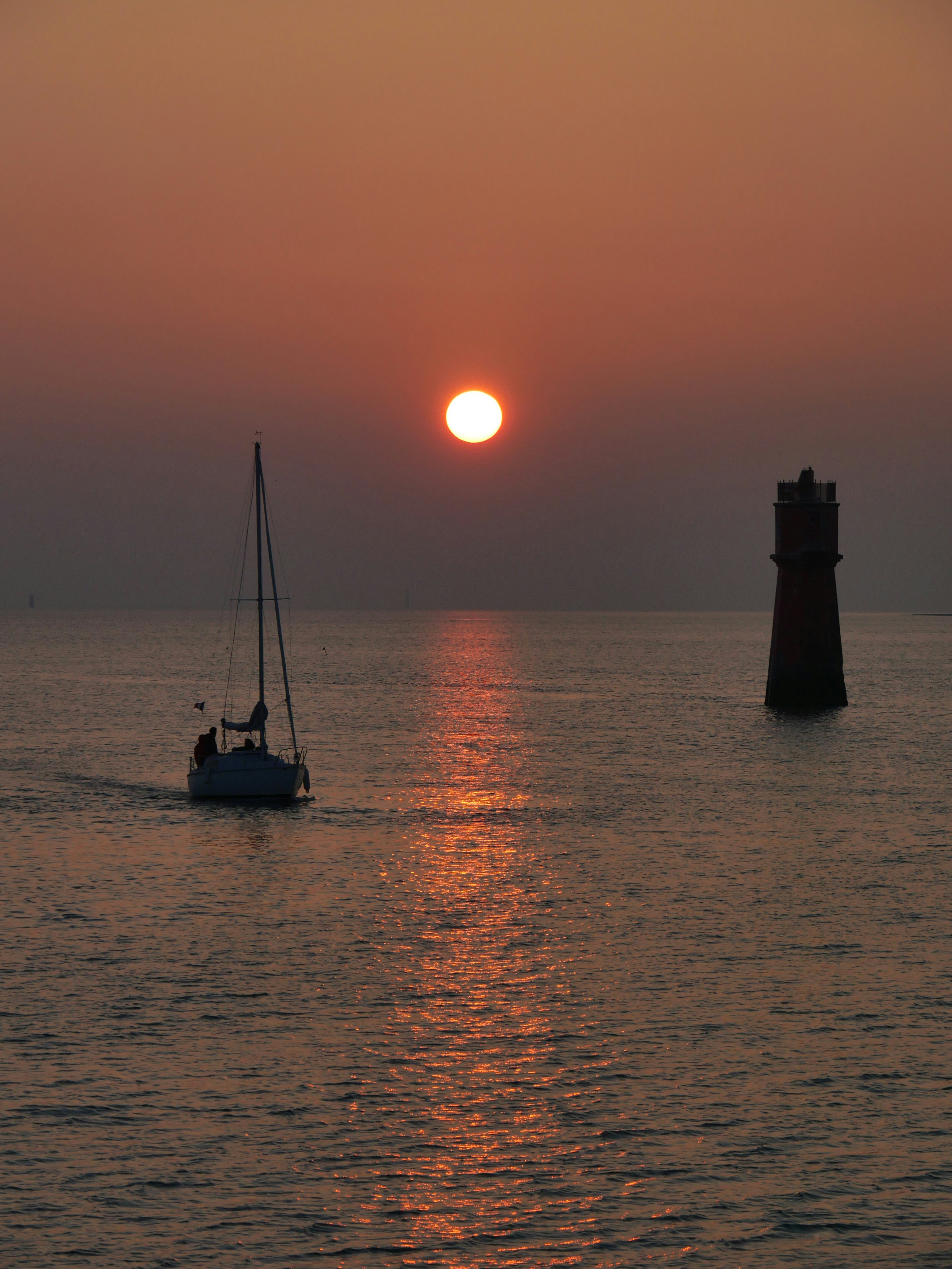 Crimson Hour: A Sailboat and Lighthouse Stand Guard at Dusk