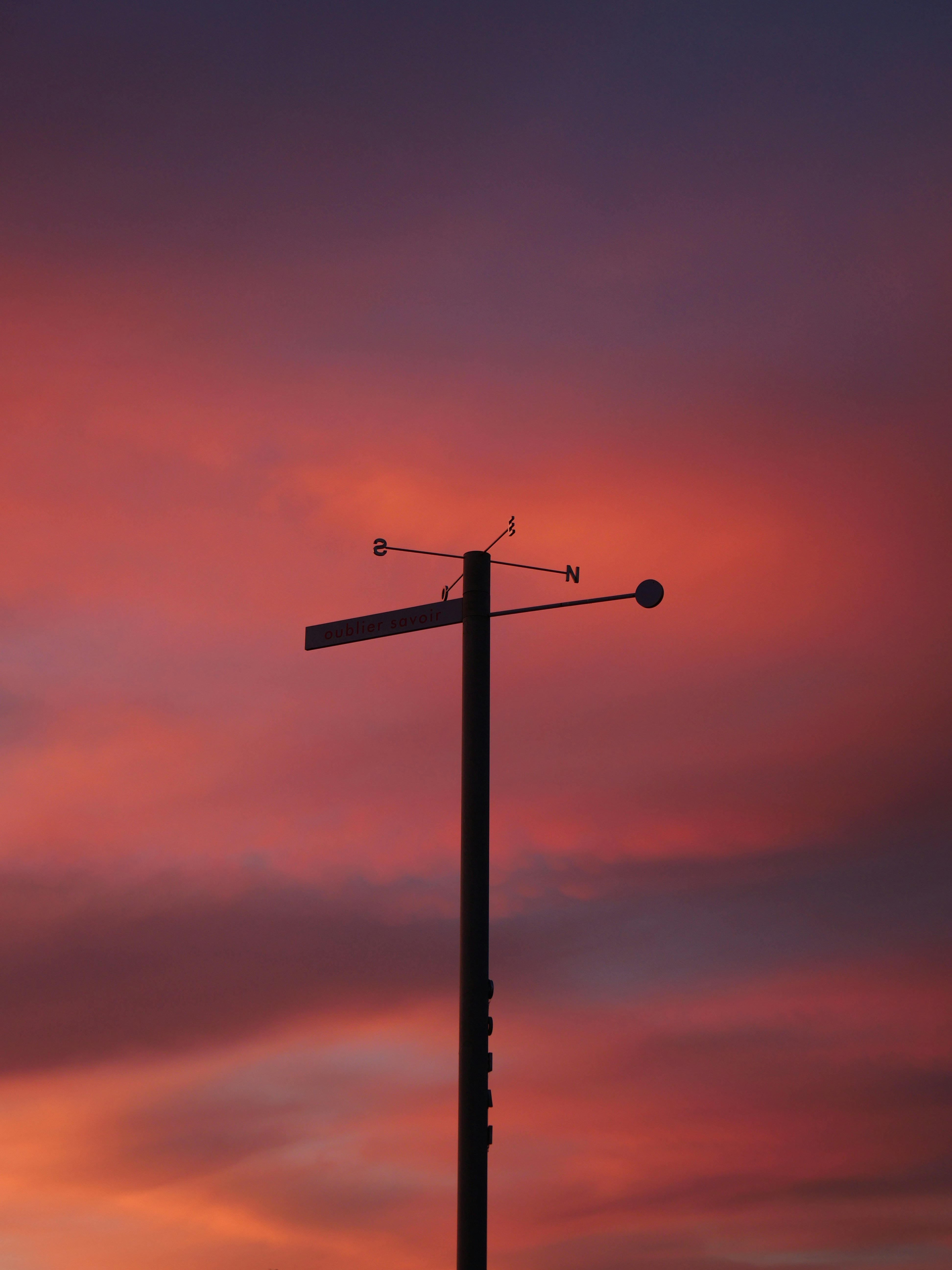 Silhouette of a weather vane against a velvet sunset sky, with warm orange-pink tones.
