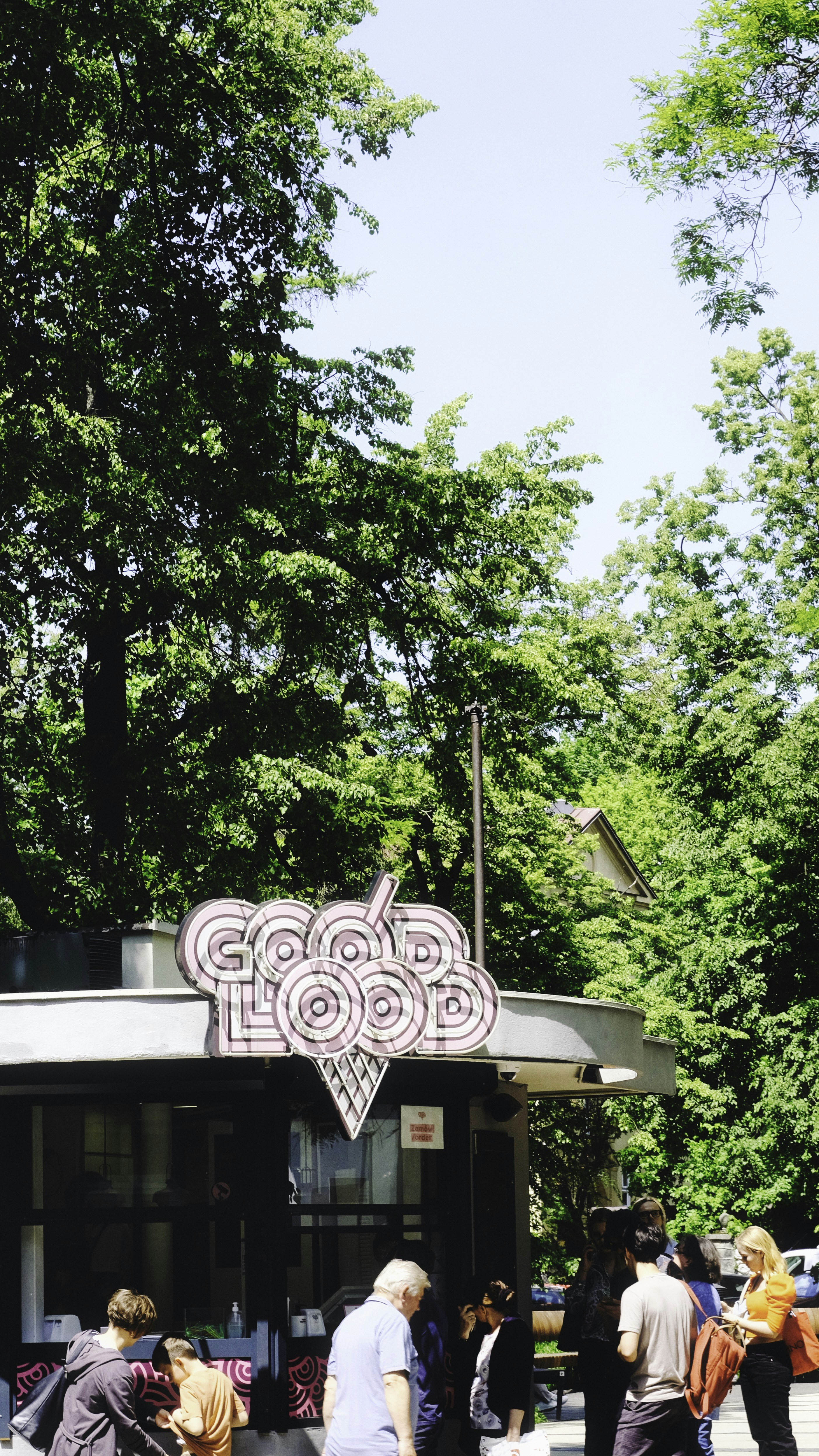 Neon Good Food Sign Framing a Sunlit Café Amid Green Canopy