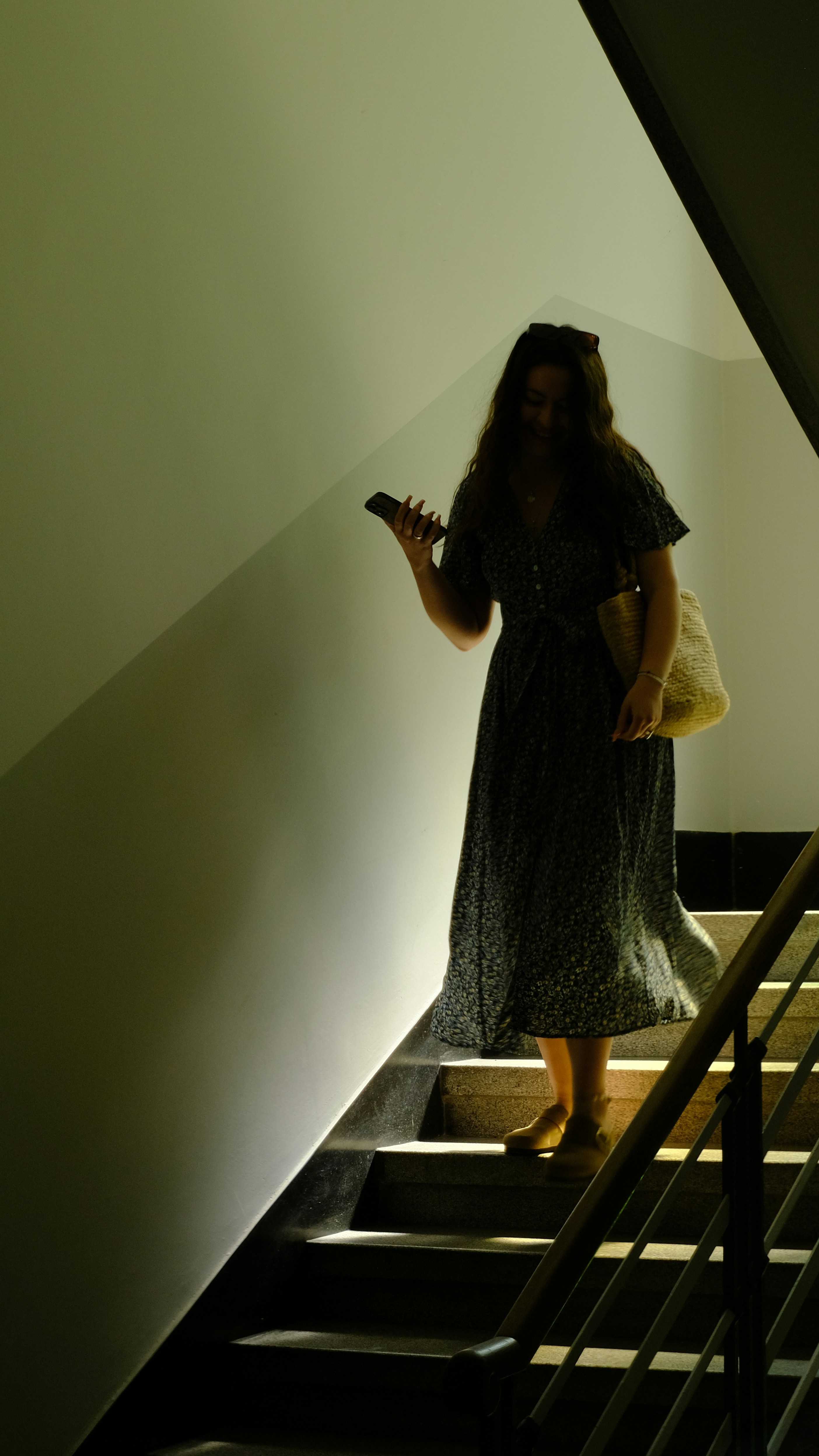 Dim Stairwell Portrait: A Woman with Phone Descends a Shadowed Staircase