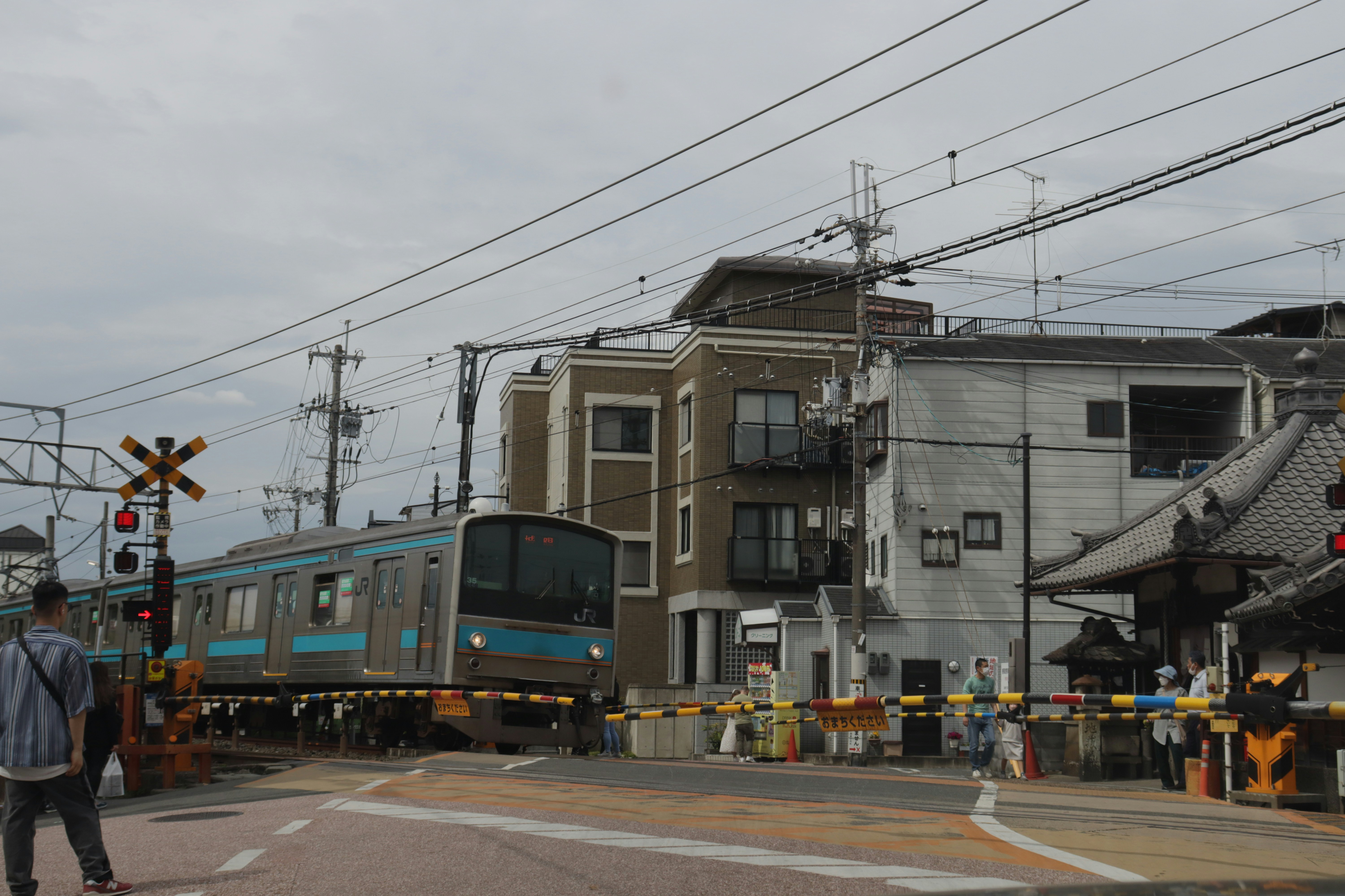 Blue Commuter at a City-Level Crossing, Framed by Wires and Brick