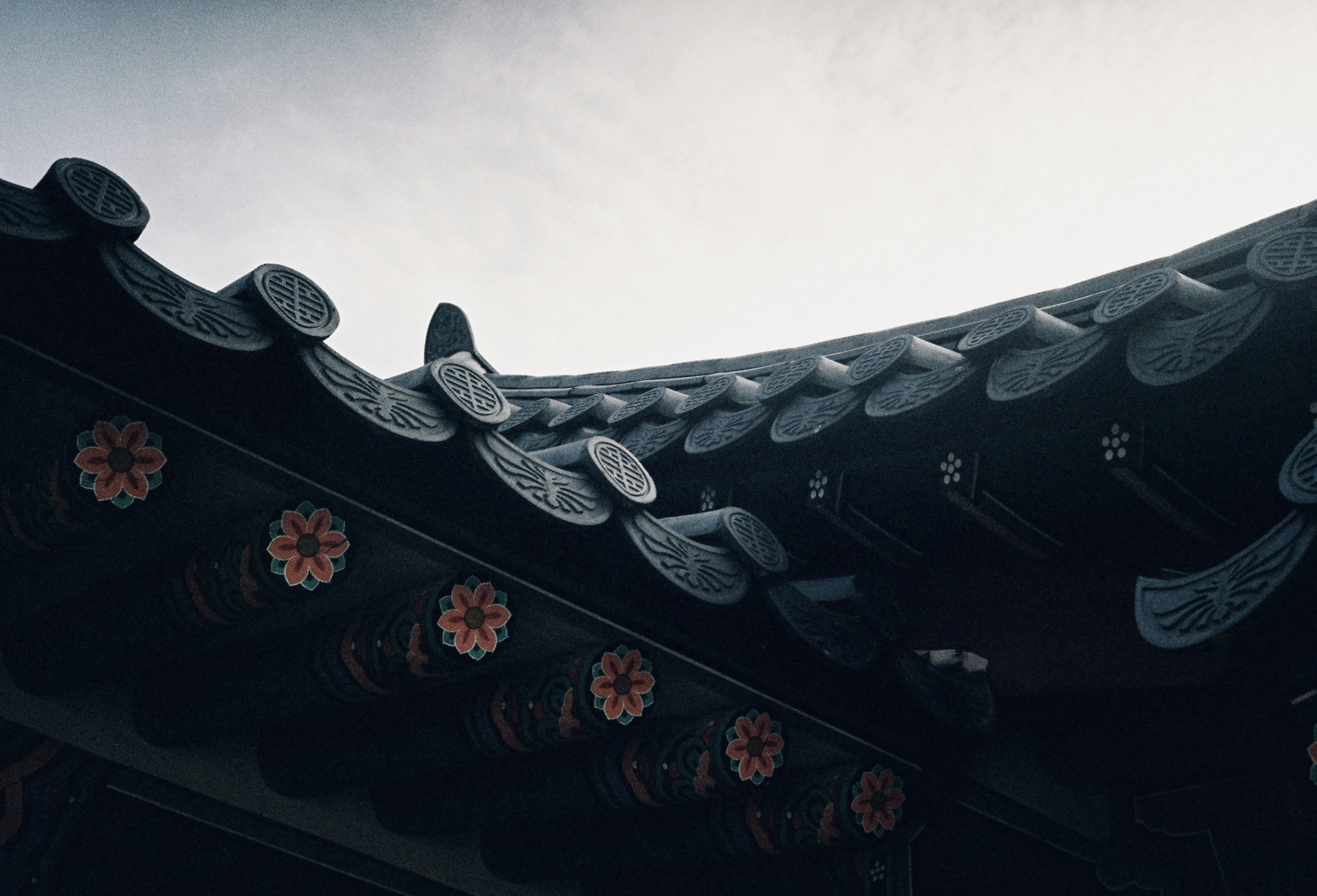 Crimson Blossoms Trim the Eaves of a Shadowed Tile Roof