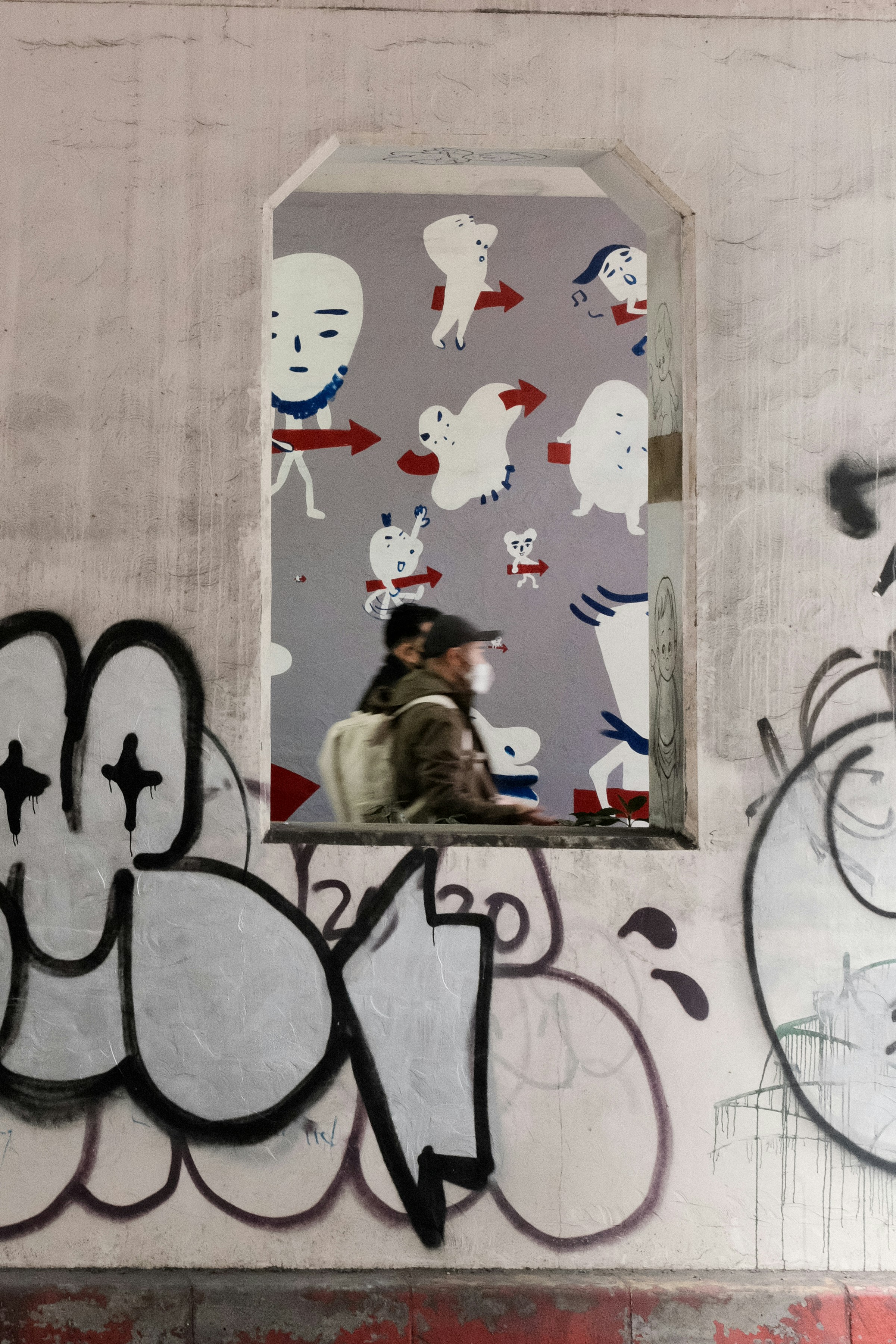 Through the Graffiti Window: A Blurred Pedestrian Amid Arrows and White Creatures