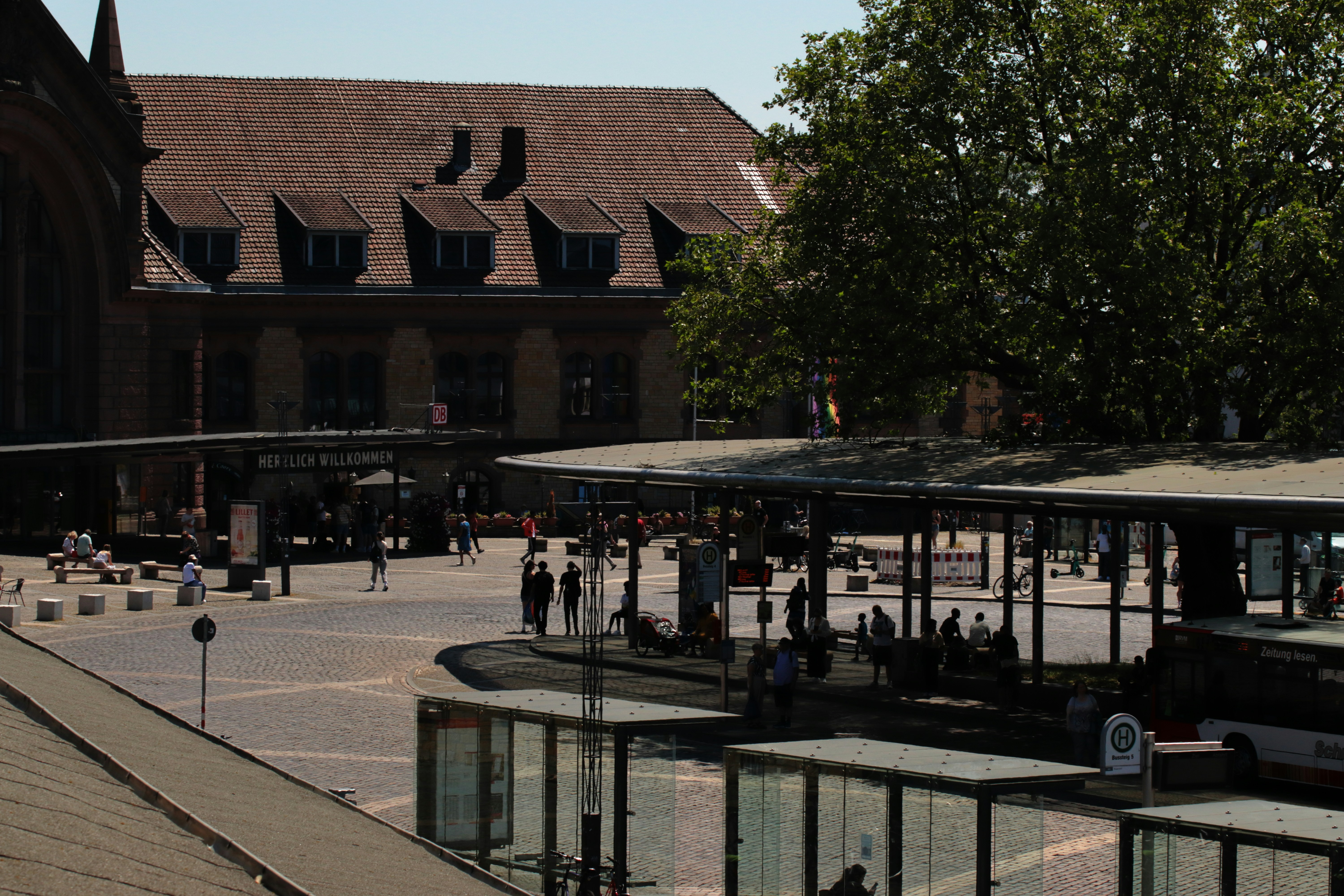 Sunlit European Square: Terracotta Roofs, Glass Railings, and People in Motion
