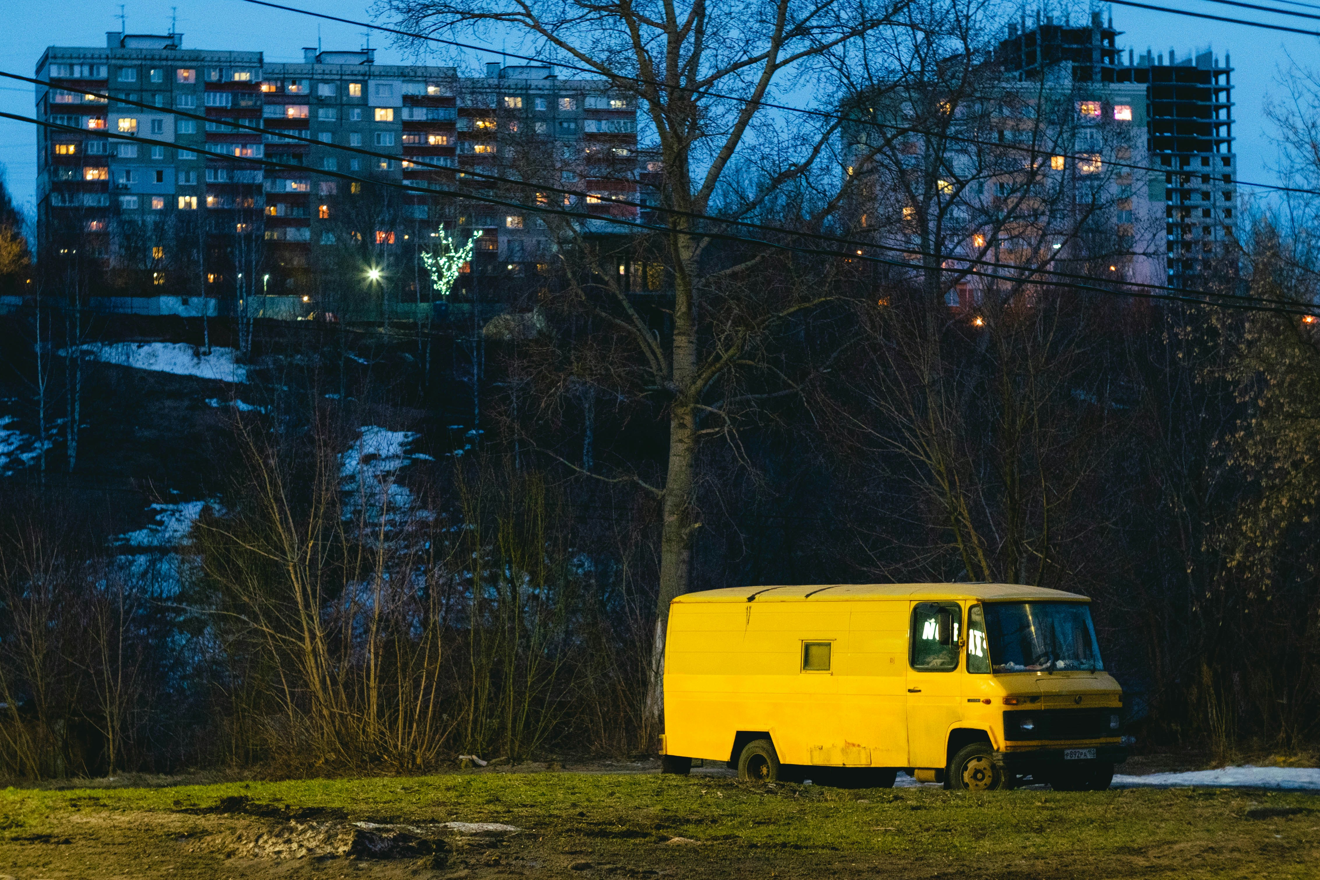 Blue Hour Contrast: Yellow Van in a Quiet Field Against the City Horizon