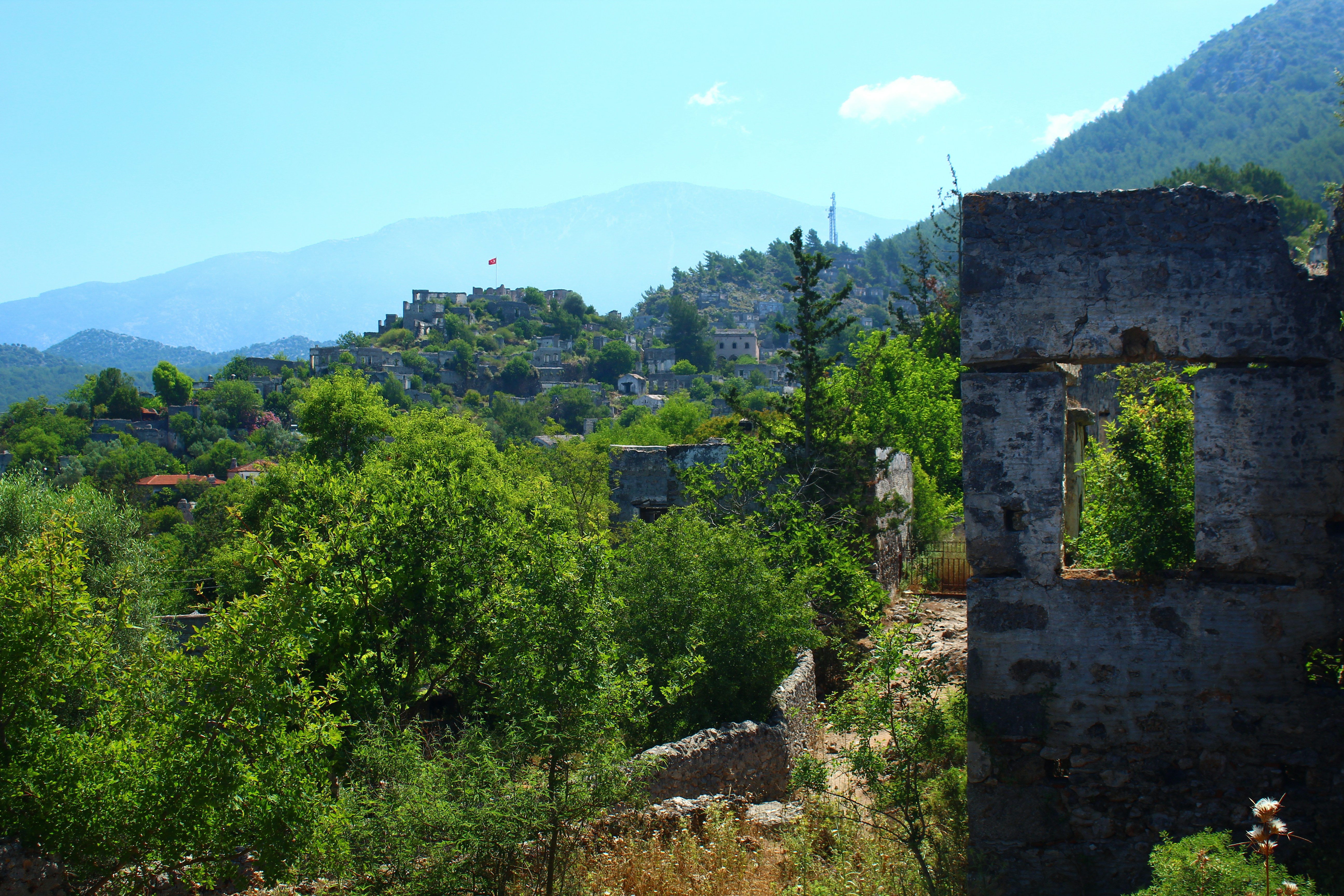 Ruined stone structure amidst lush green landscape with distant mountains under a clear blue sky.