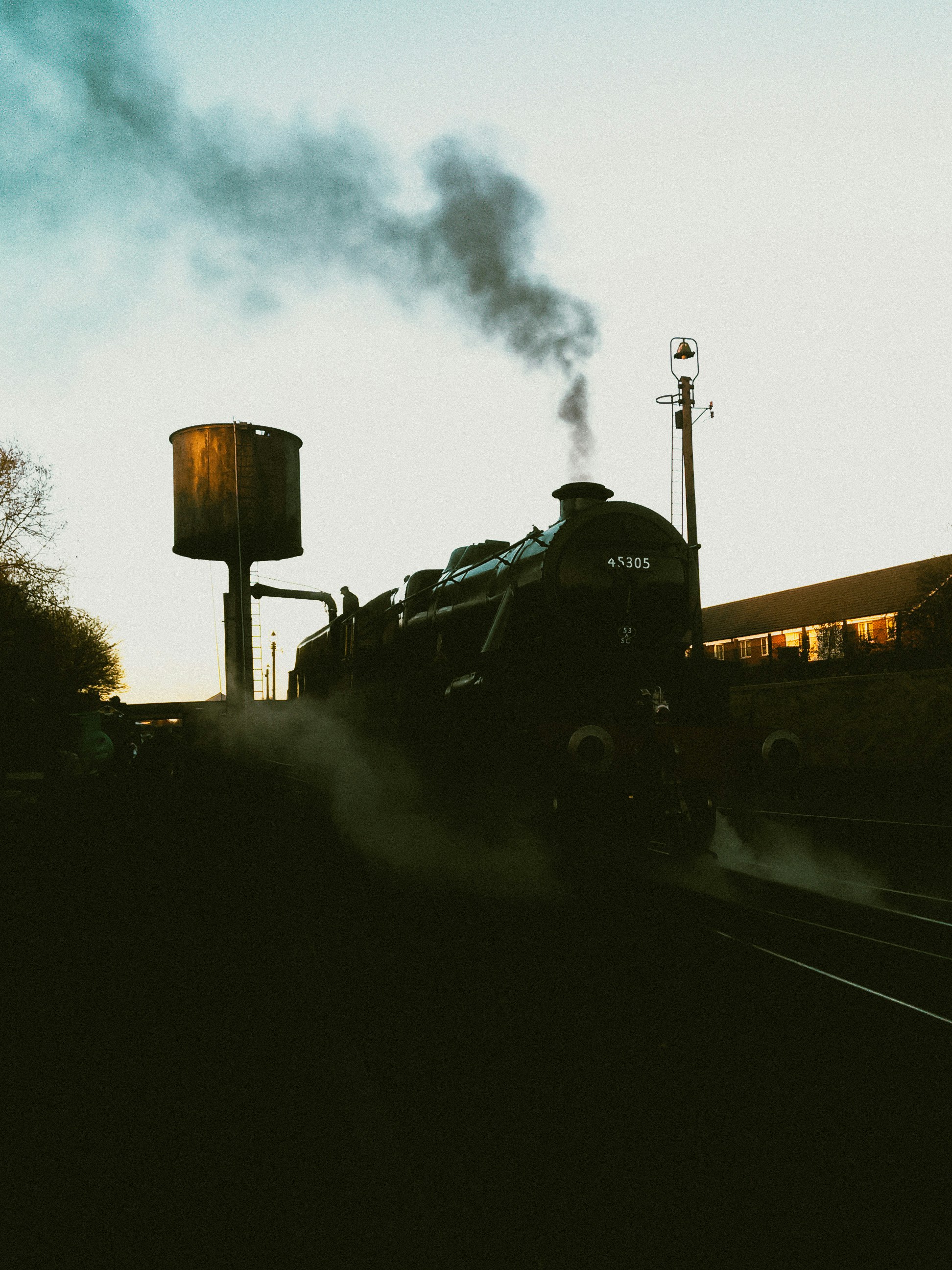 A train traveling down train tracks next to a water tower photo – Free ...